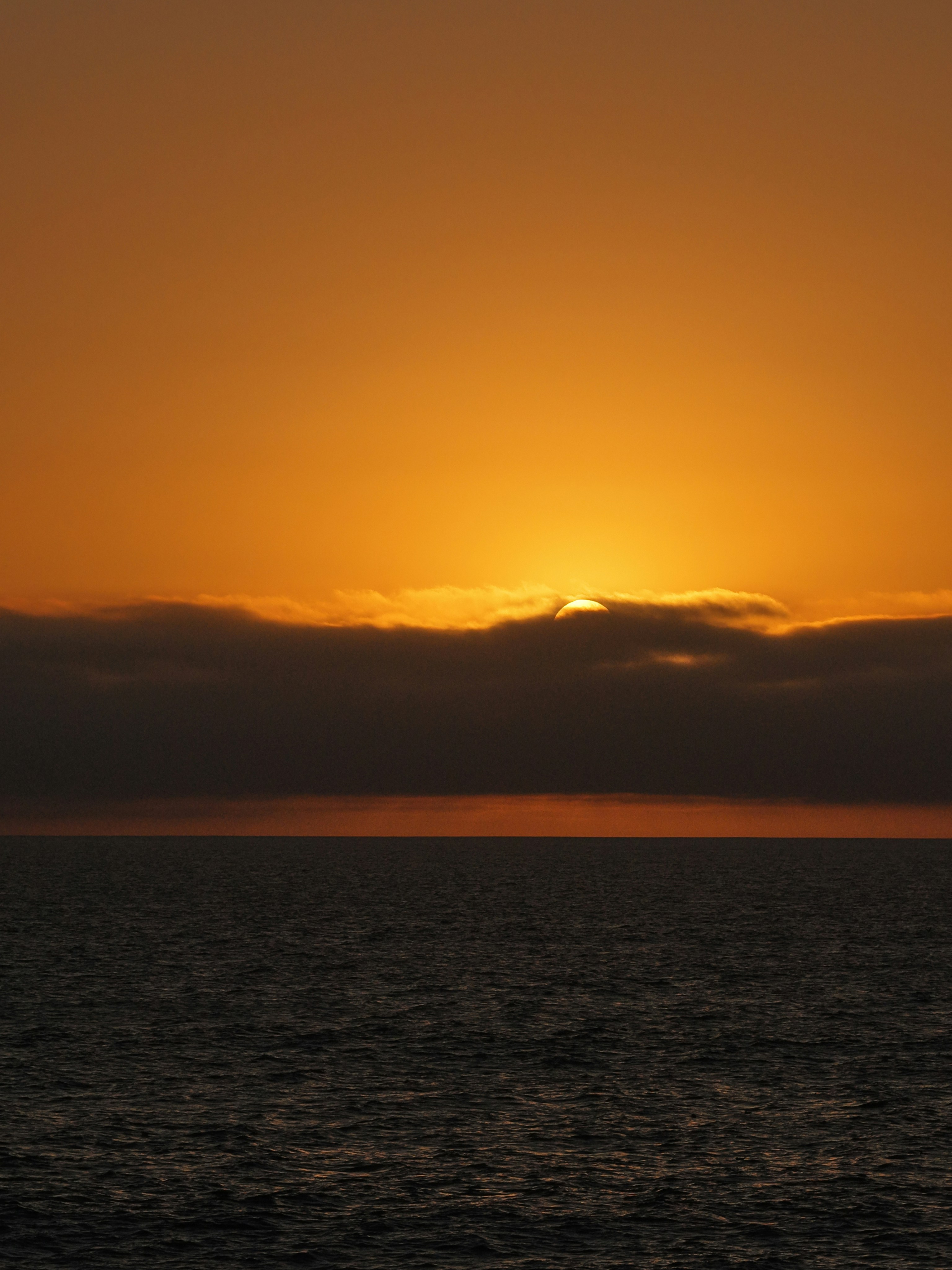 Golden sunset illuminating the ocean, with the sun partially hidden behind clouds. The tranquil scene evokes a sense of calm and reflection.