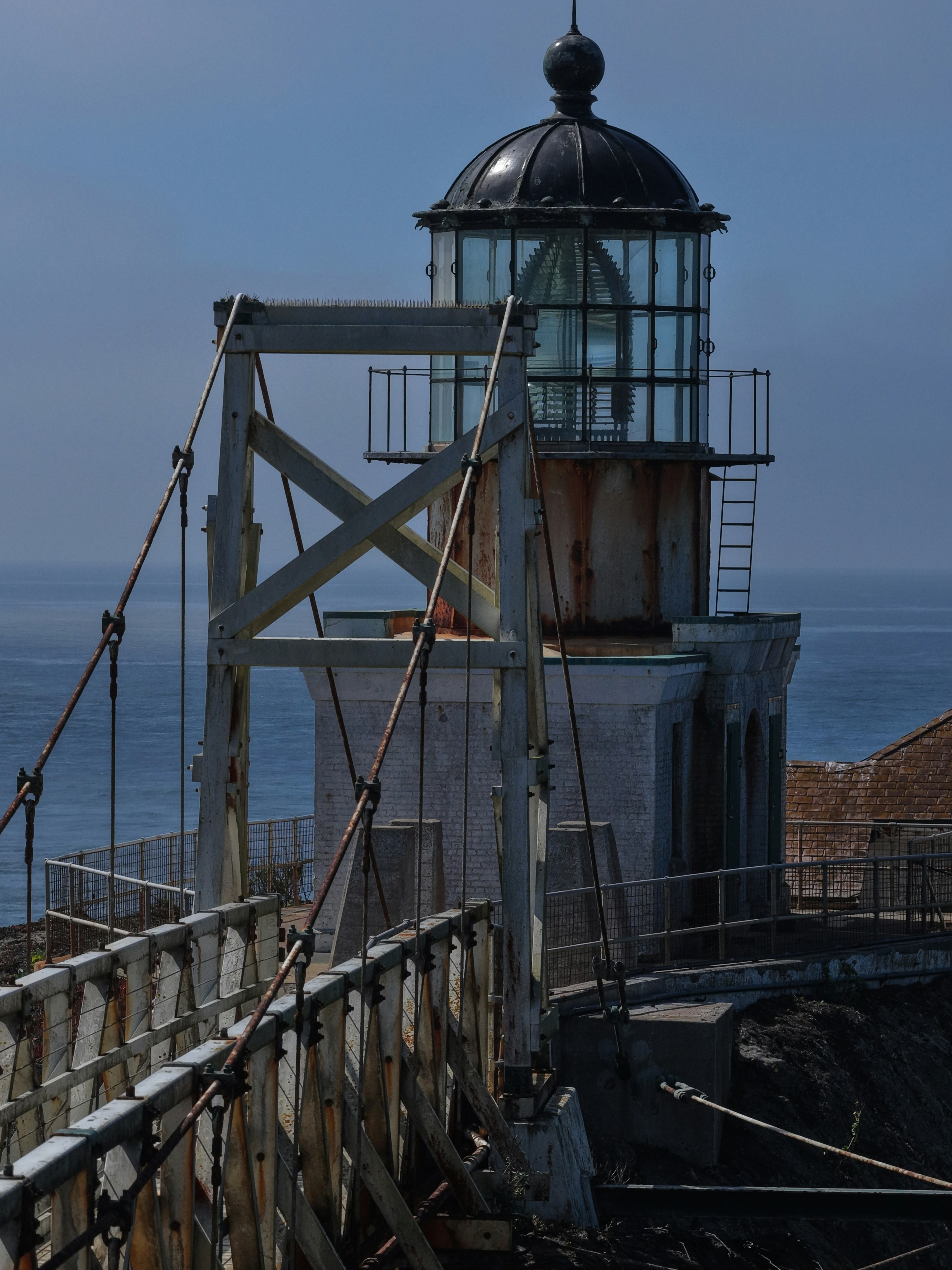 Weathered lighthouse perched on a cliff, overlooking the ocean, with a bridge leading to its base.