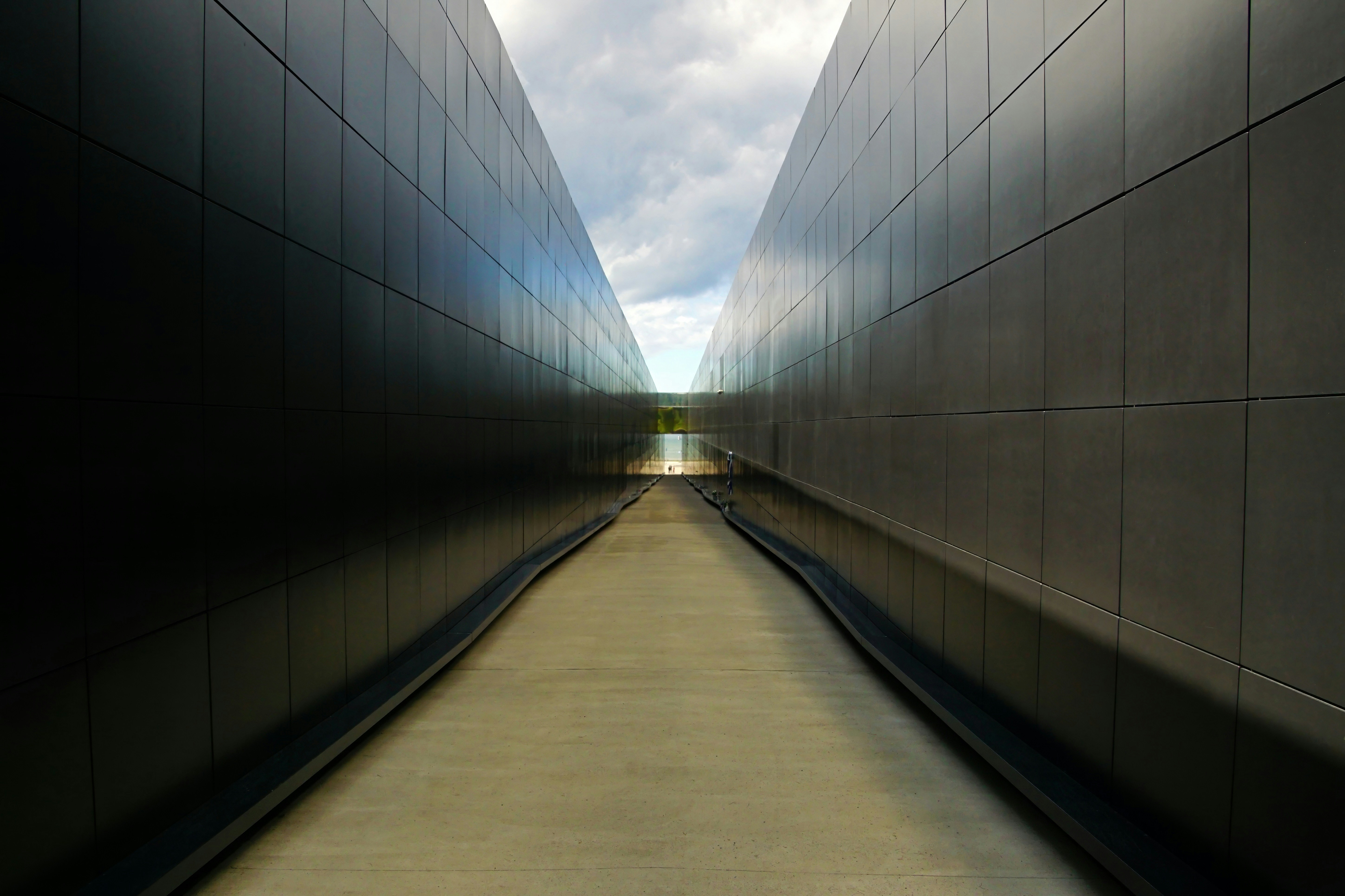 The Estonian Memorial to the Victims of Communism in Tallinn, Estonia. | A pathway between two dark, modern walls leading to sky.