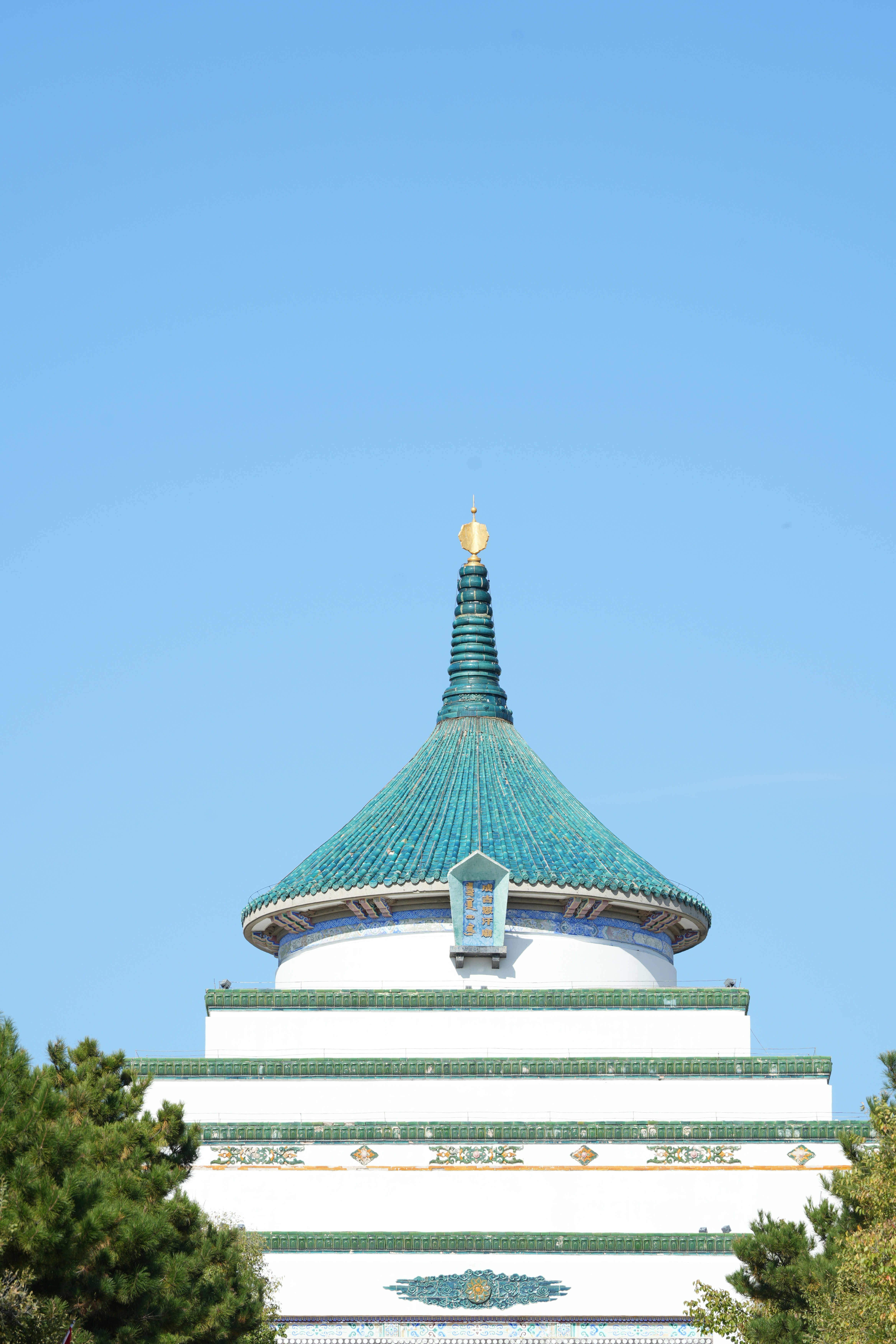 Ornate pagoda with a striking green roof and golden finial against a clear blue sky.