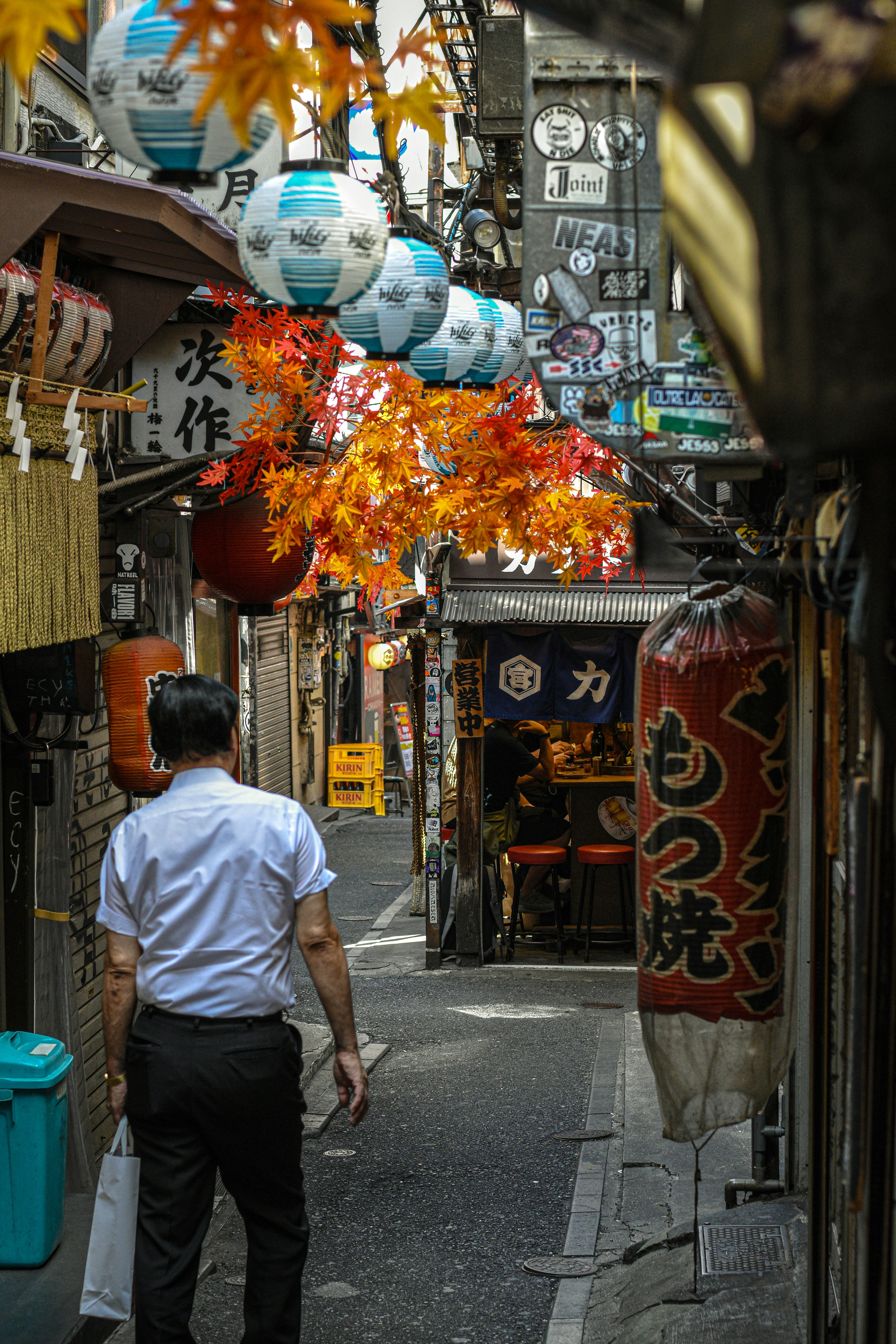 Man walks down a narrow street with lanterns.