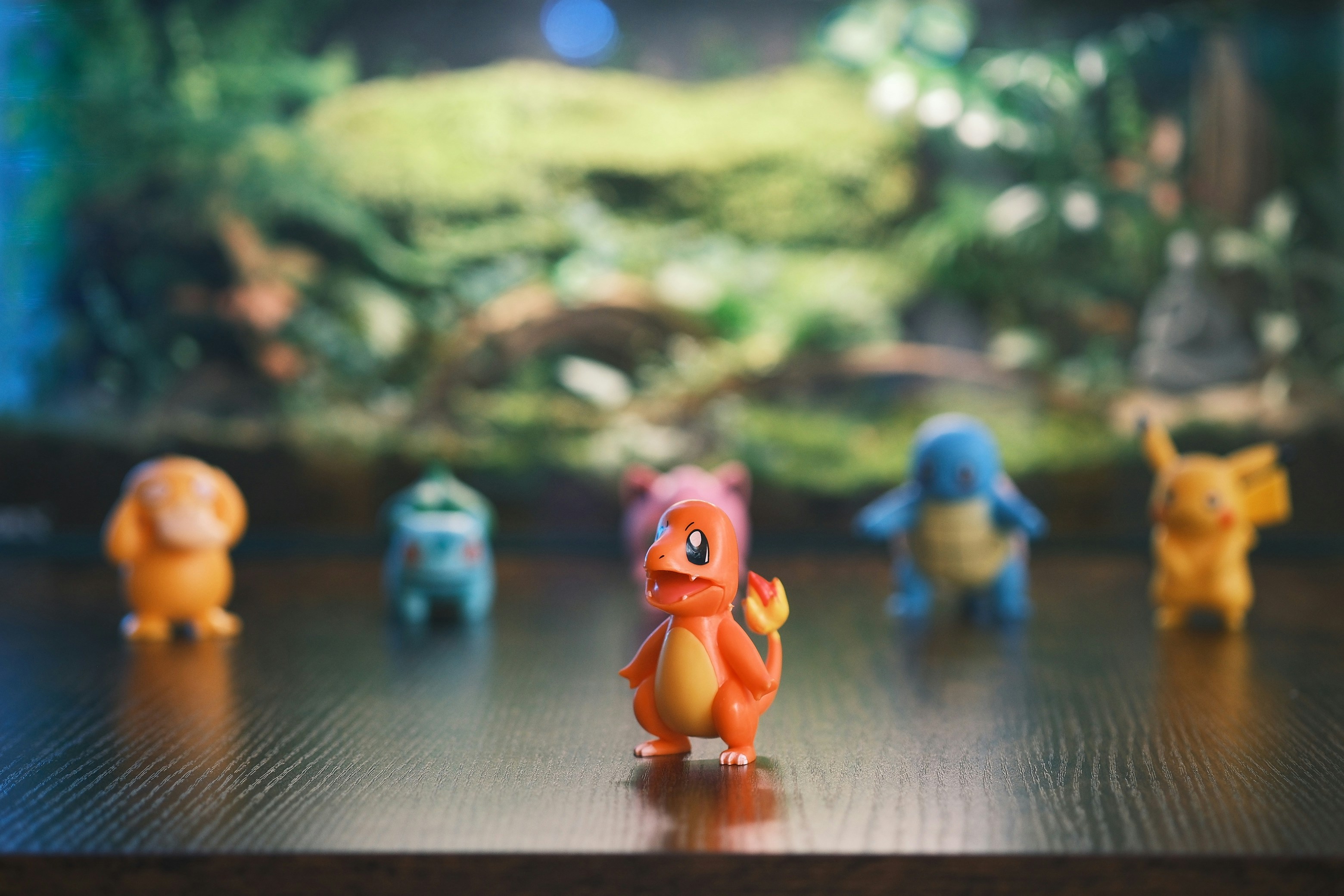 Charmander stands proudly in the foreground, surrounded by a playful assembly of Pokémon figurines in a vibrant, nature-inspired setting.