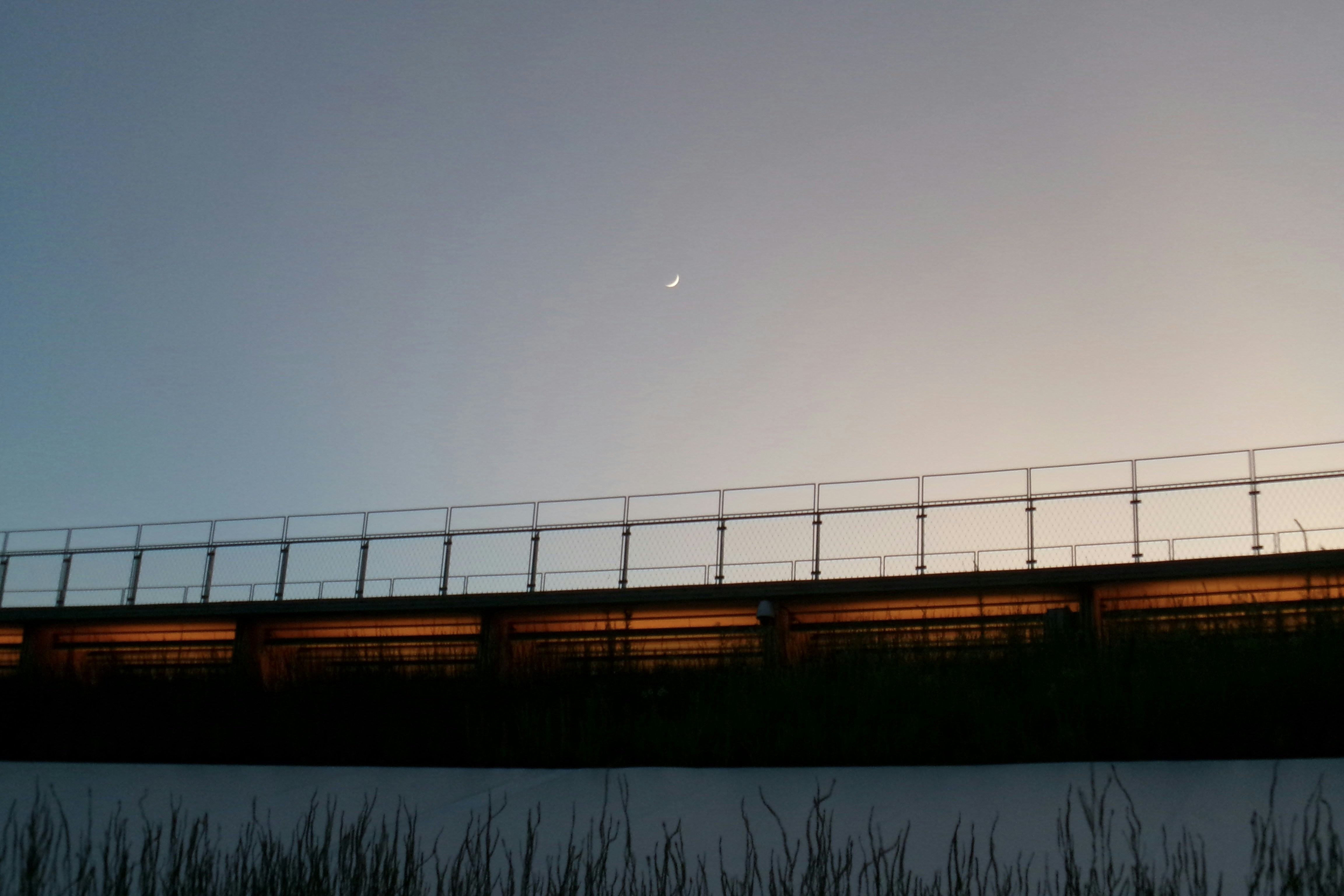 KODAK Digital Still Camera | Crescent moon in a pale sky over a bridge.