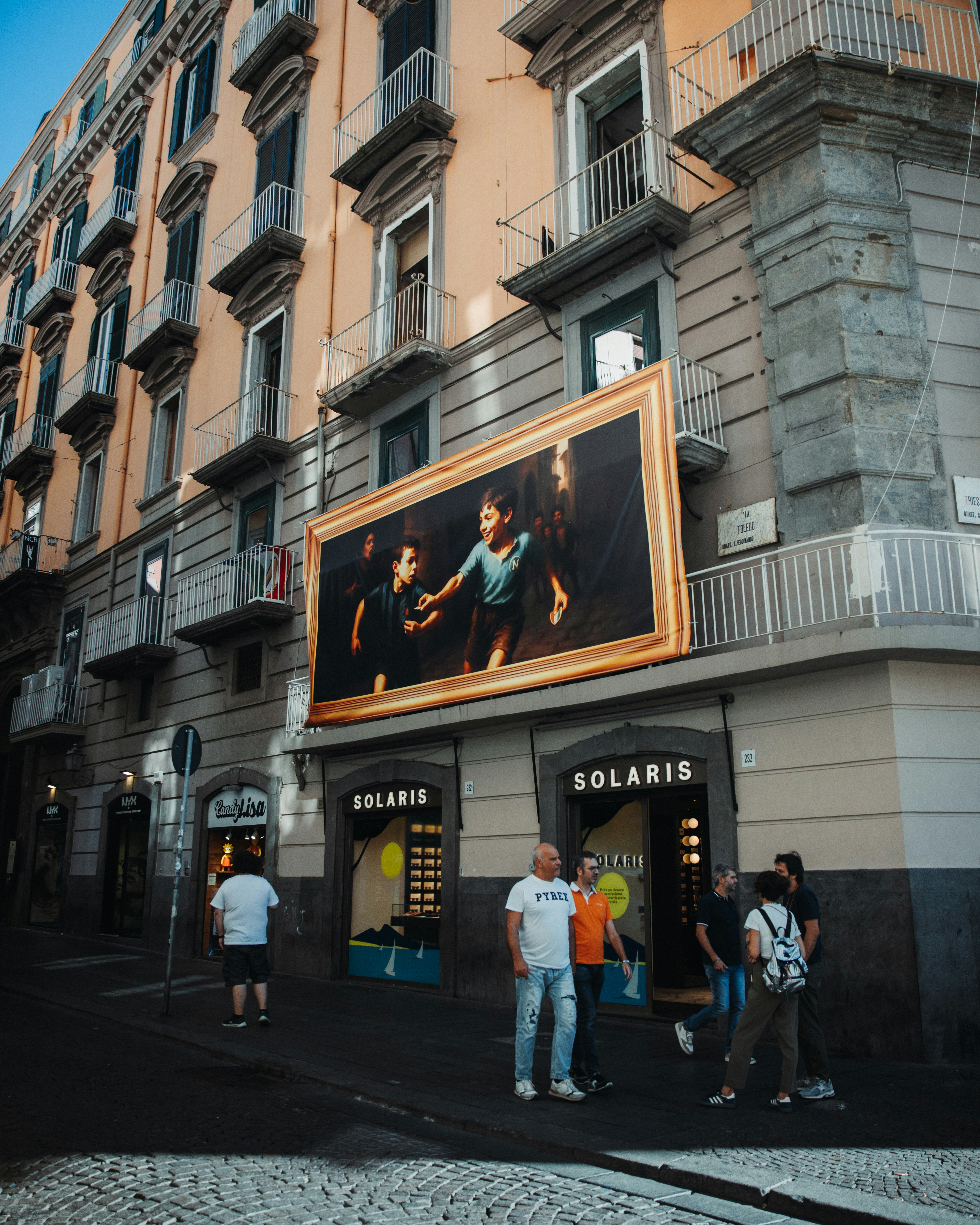 Large framed artwork displayed on building facade above shops.