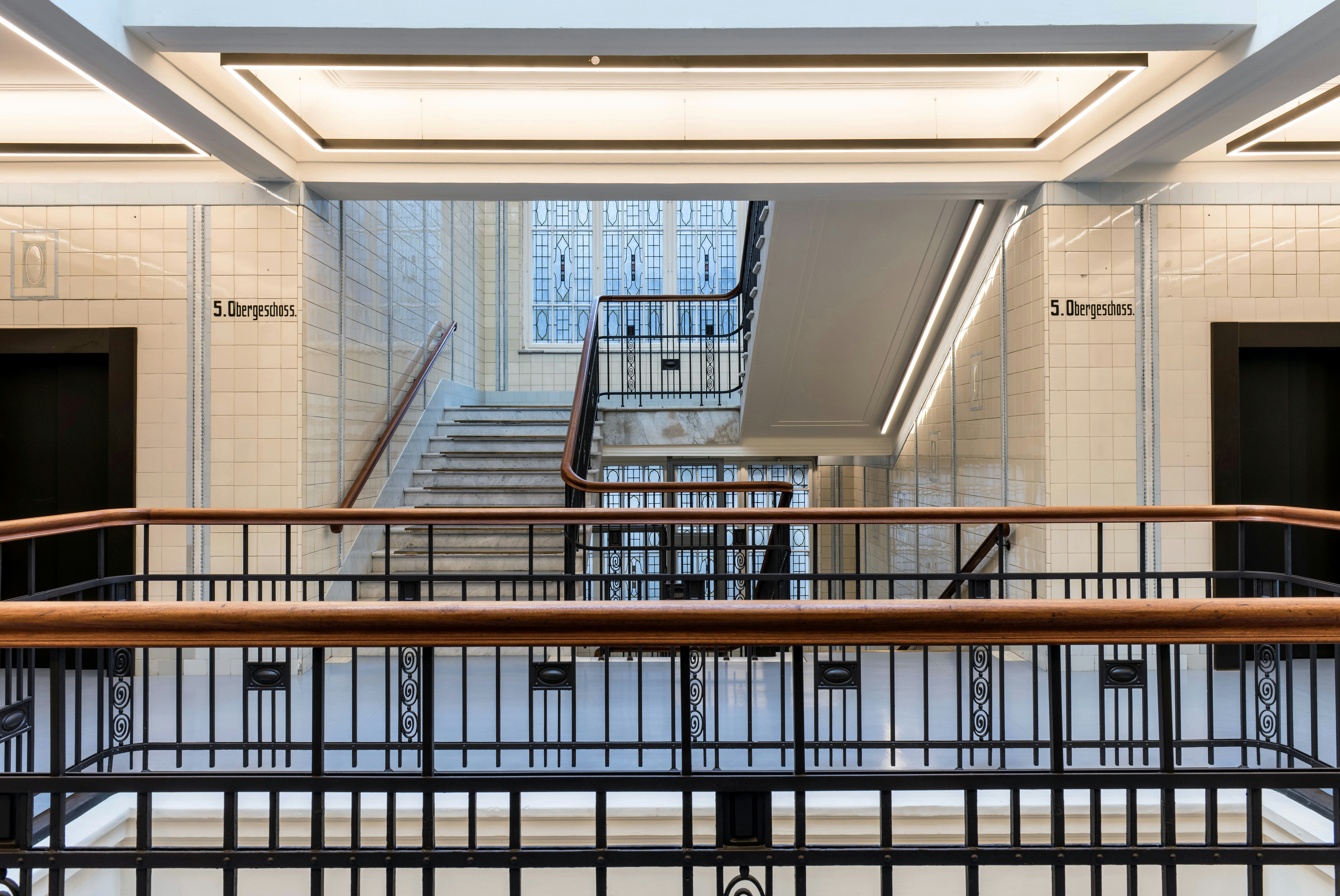 Elegant interior staircase framed by modern railings and illuminated by natural light streaming through large windows.