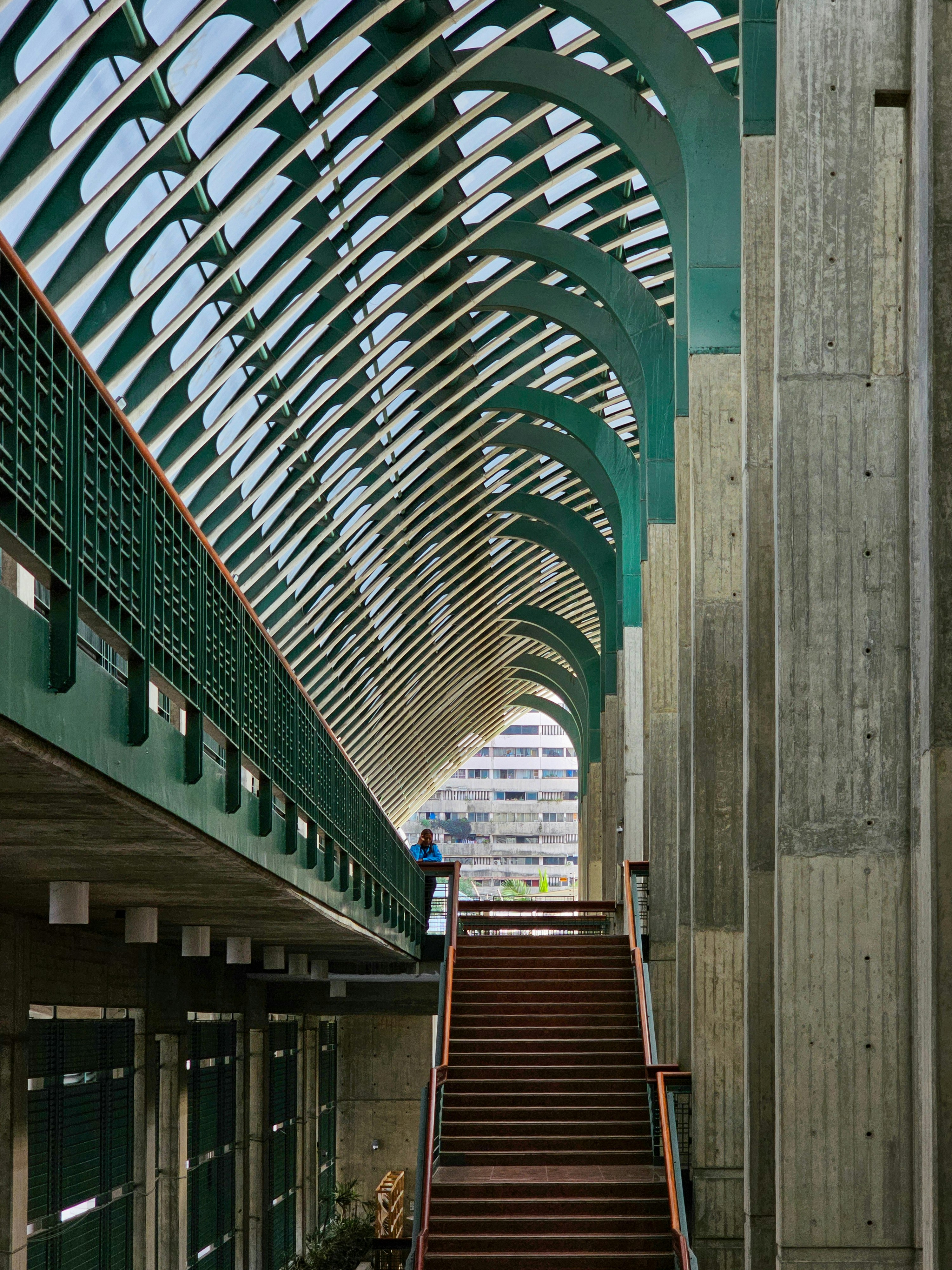 Modern architectural interior featuring a series of curved beams and a staircase leading upwards, with a person standing on the upper level.