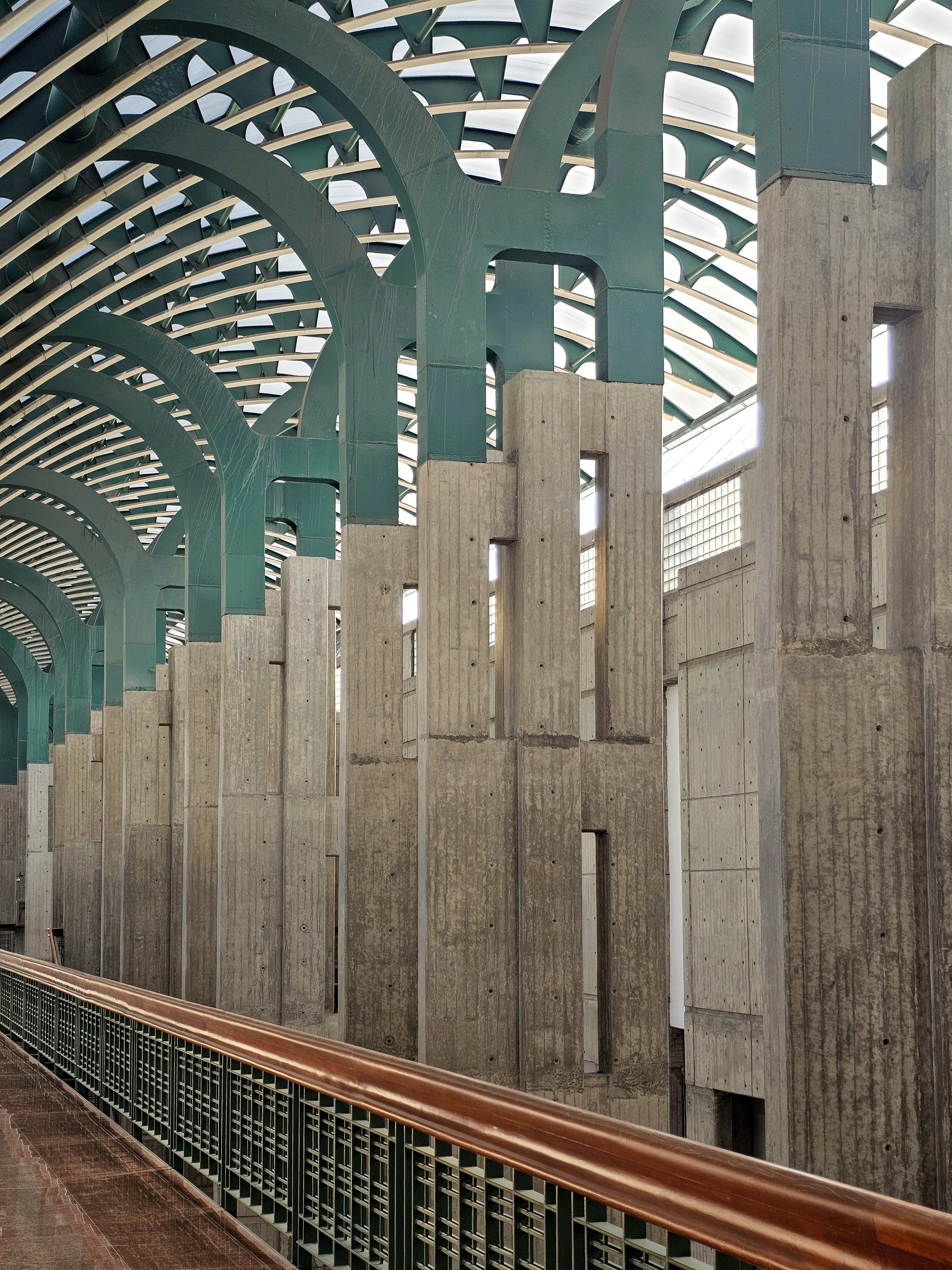 A modern architectural interior showcasing a blend of concrete pillars and green arches, emphasizing structural elegance and design innovation.