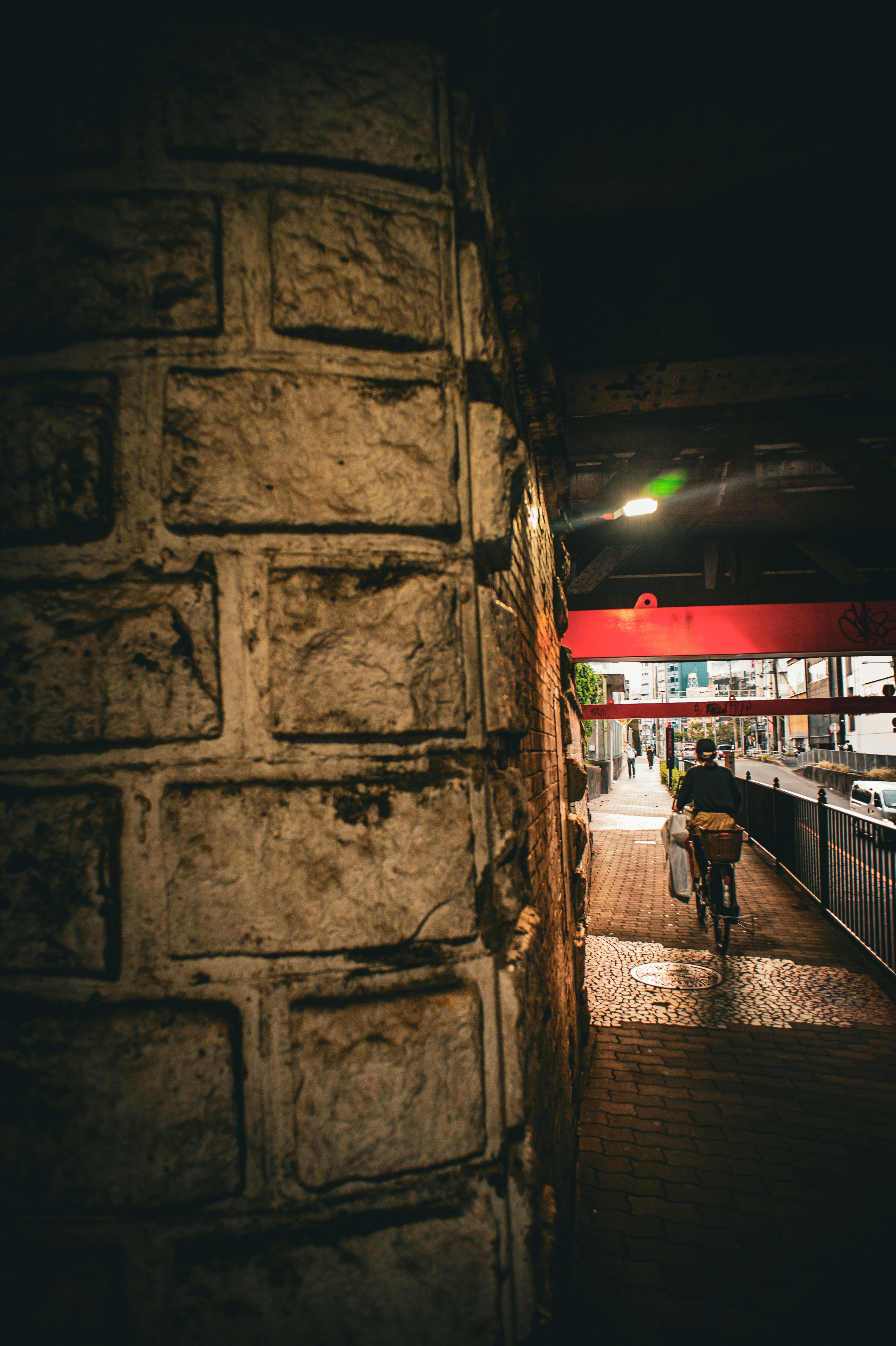 Person rides bicycle under a red bridge.