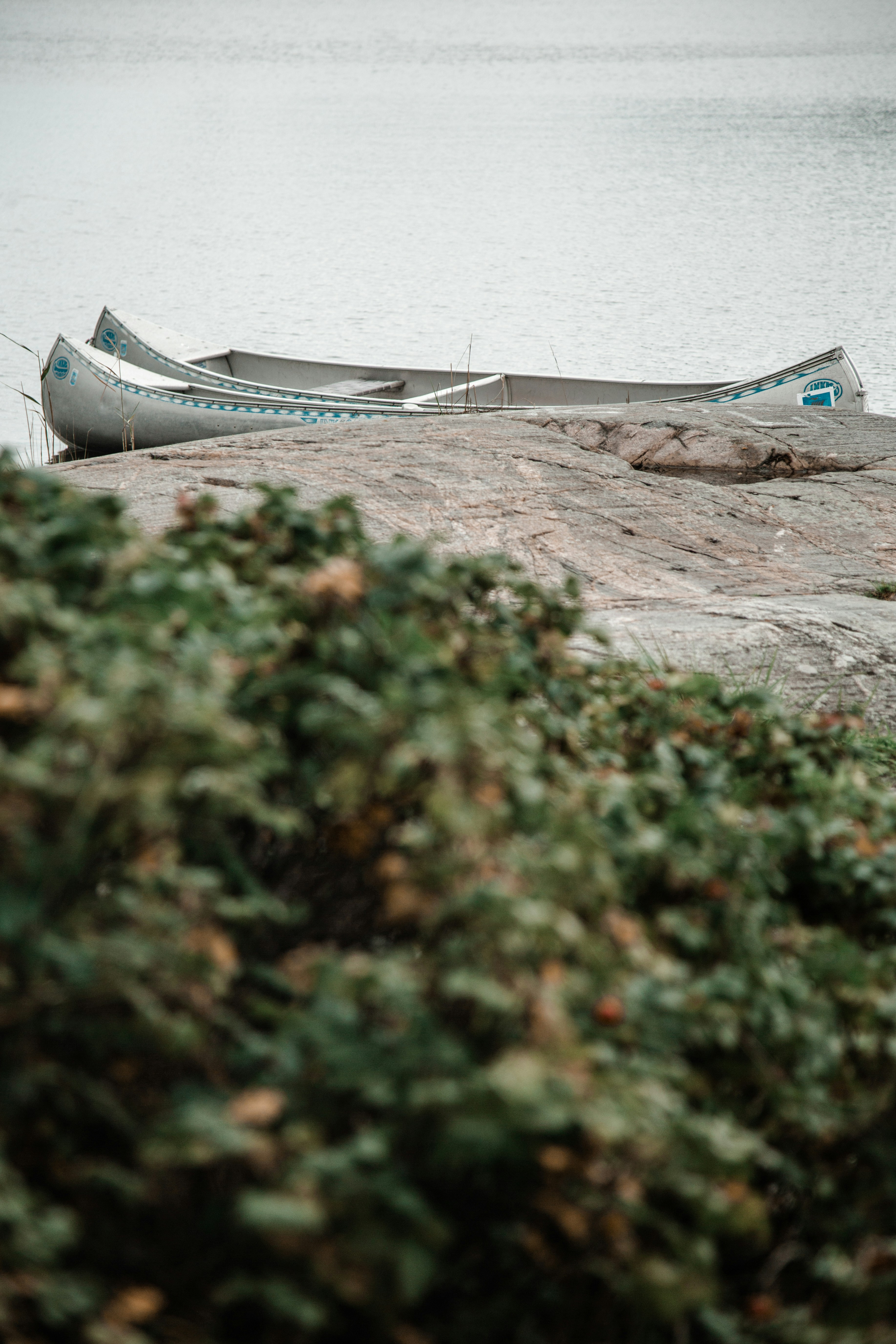 Two canoes resting on a rocky shoreline, surrounded by lush greenery and calm waters. The tranquil setting invites reflection.