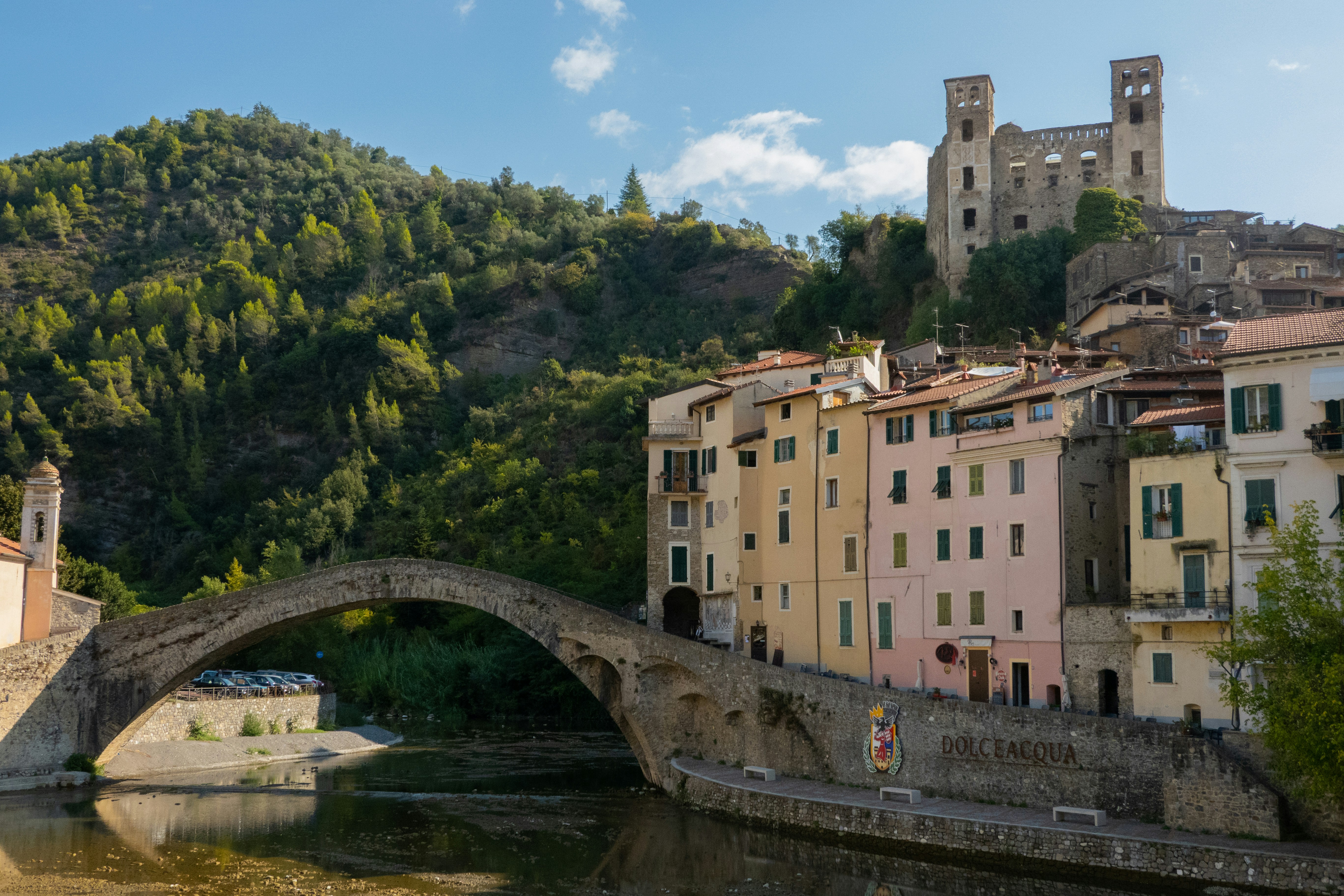 Charming riverside village with a stone bridge arching over calm waters, framed by lush hills and historical architecture.