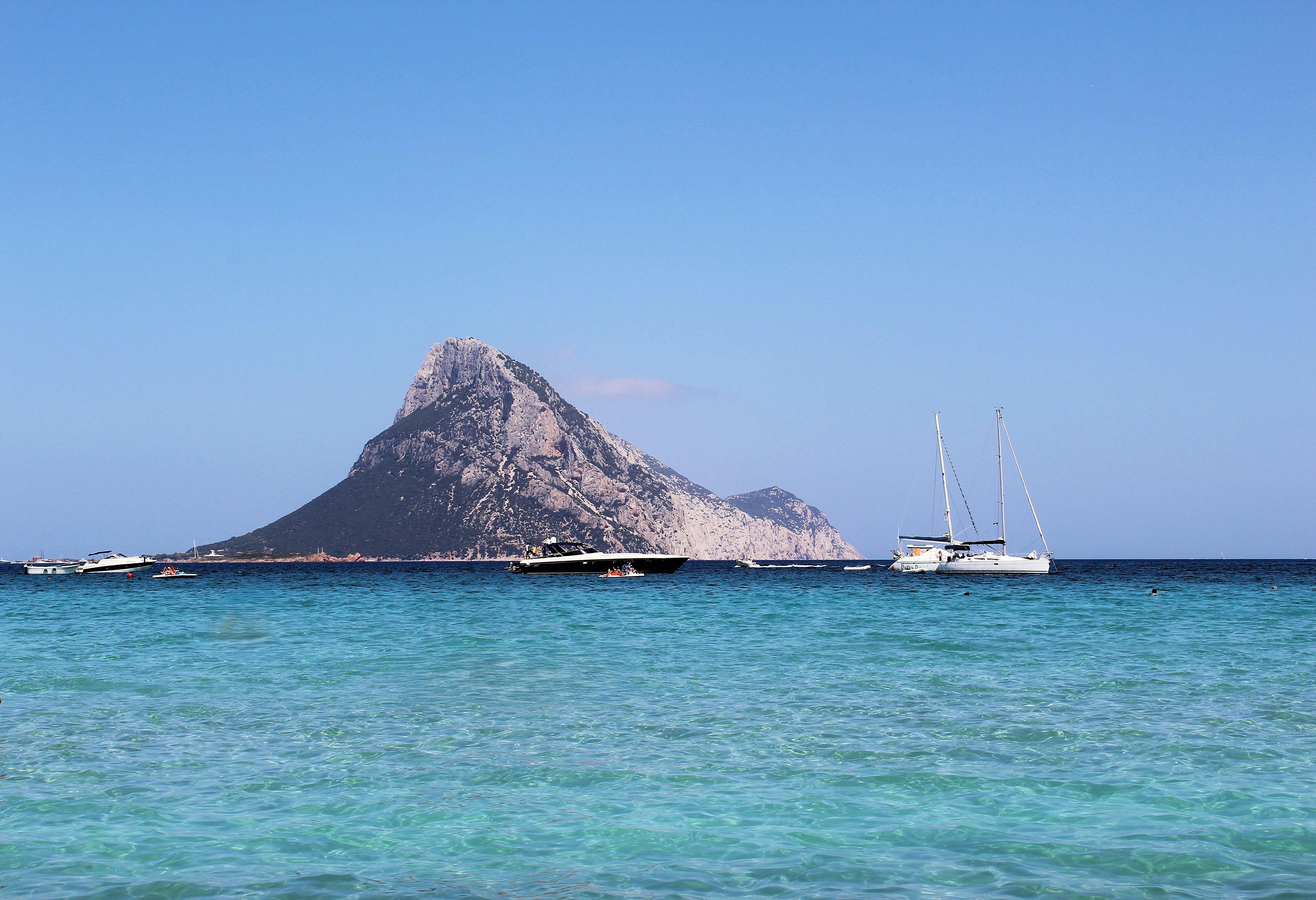 Rocky island with sailboats on turquoise sea