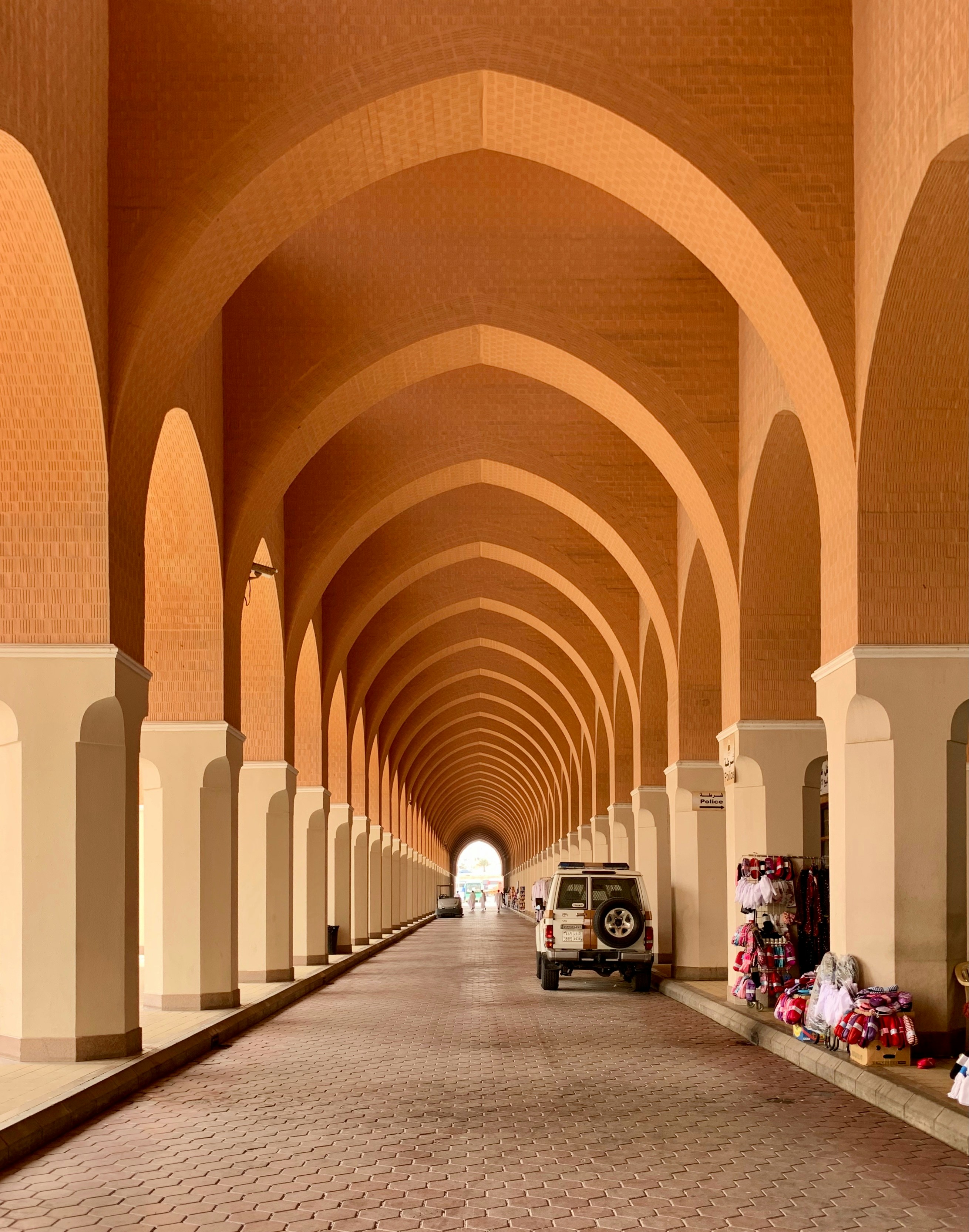 Long arched corridor with a car and market stalls