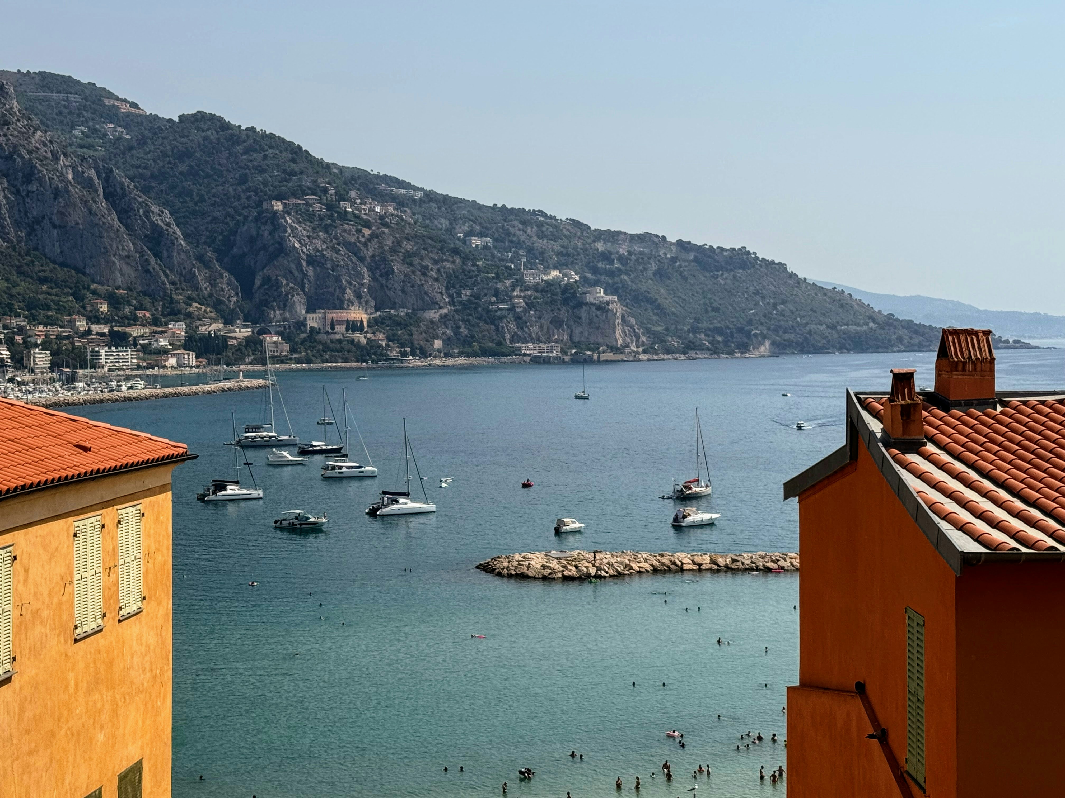 Boats anchored in a clear blue bay with coastal town.