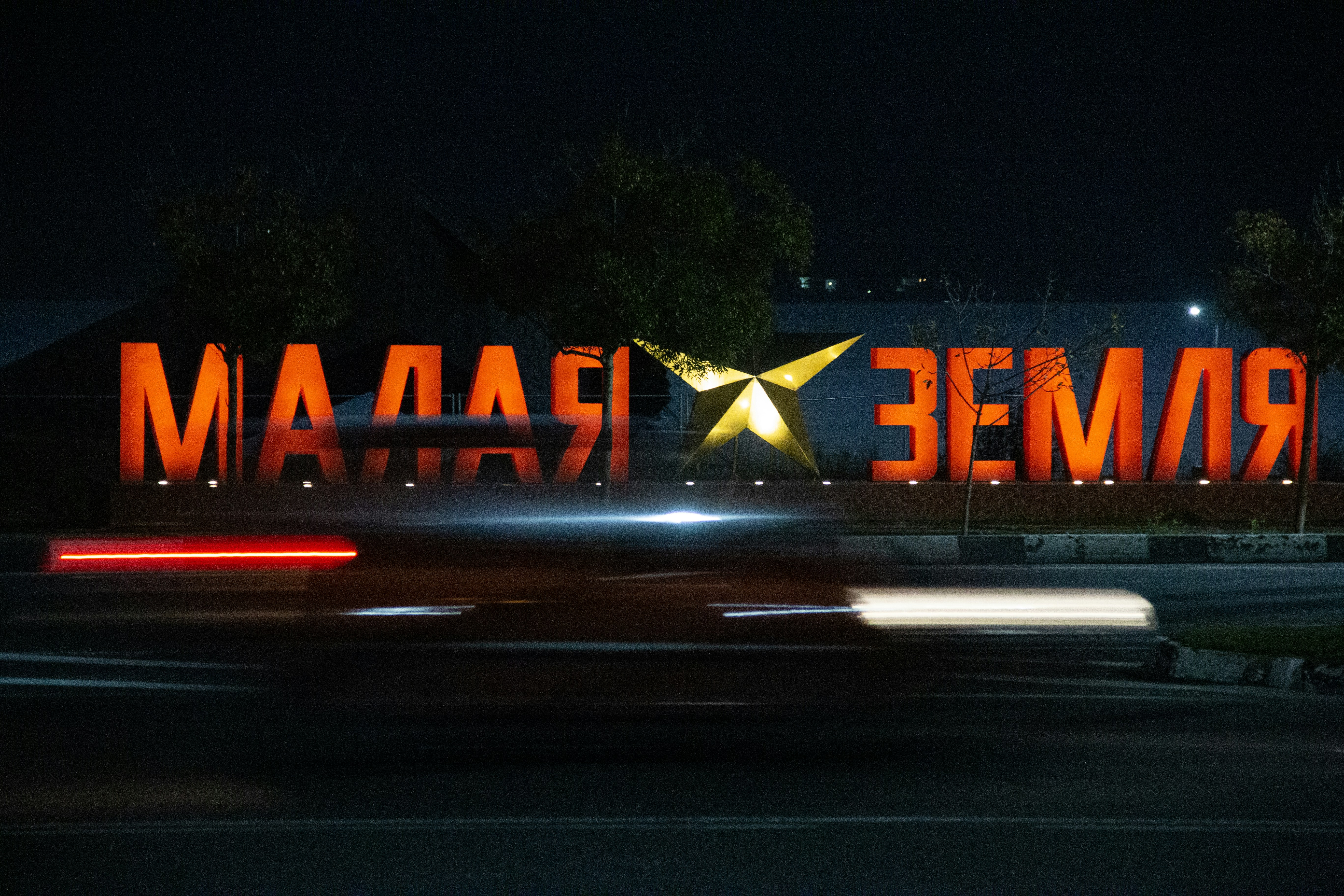 Midnight Neon Gate: Red Cyrillic Sign Framed by Streaking Vehicle Lights