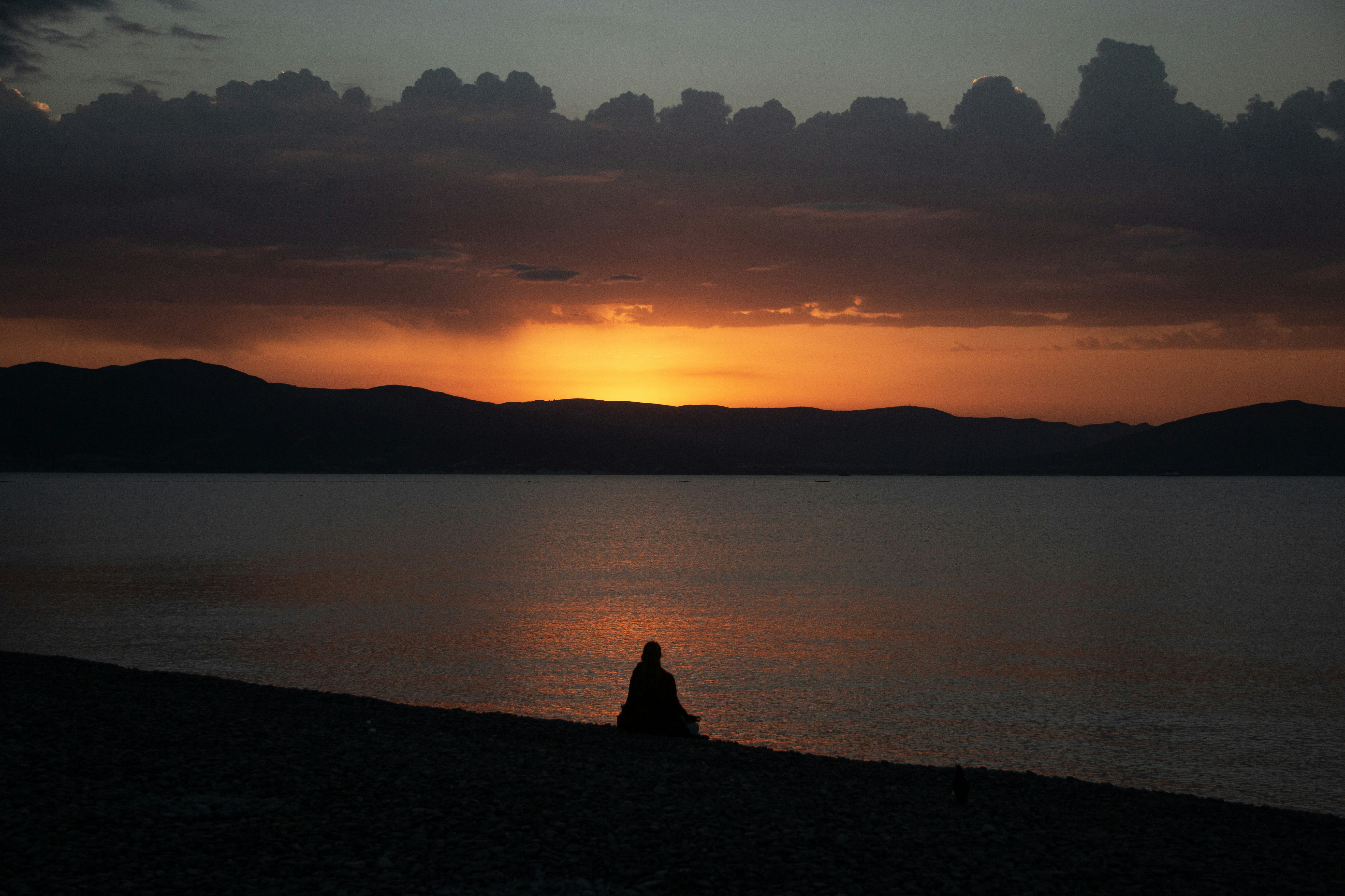 Silhouette of person watching sunset over calm water