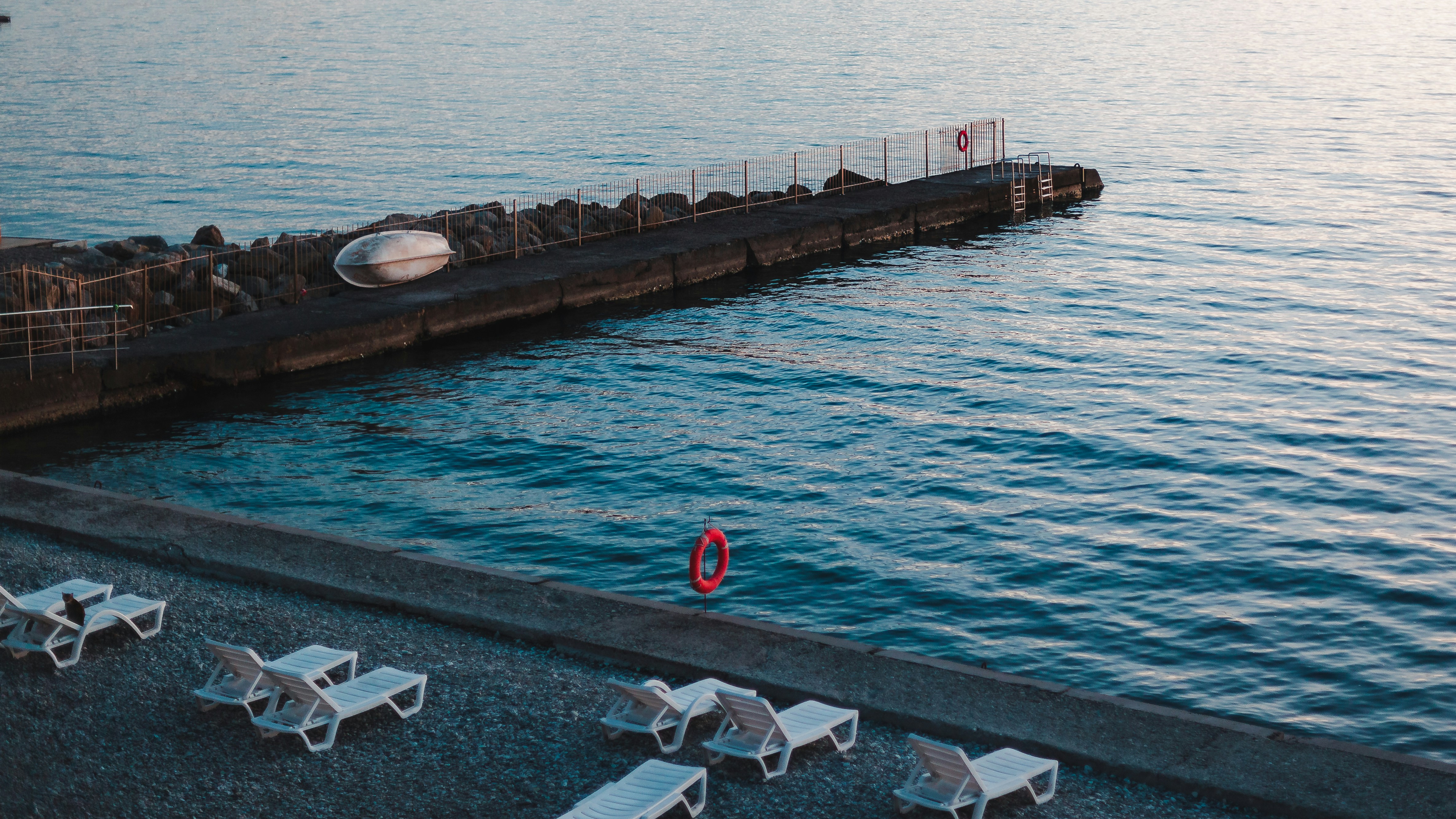 A quiet evening by the sea. Empty sun loungers and the soft light of sunset create a sense of calm and solitude. | Empty beach chairs by the ocean with a pier.