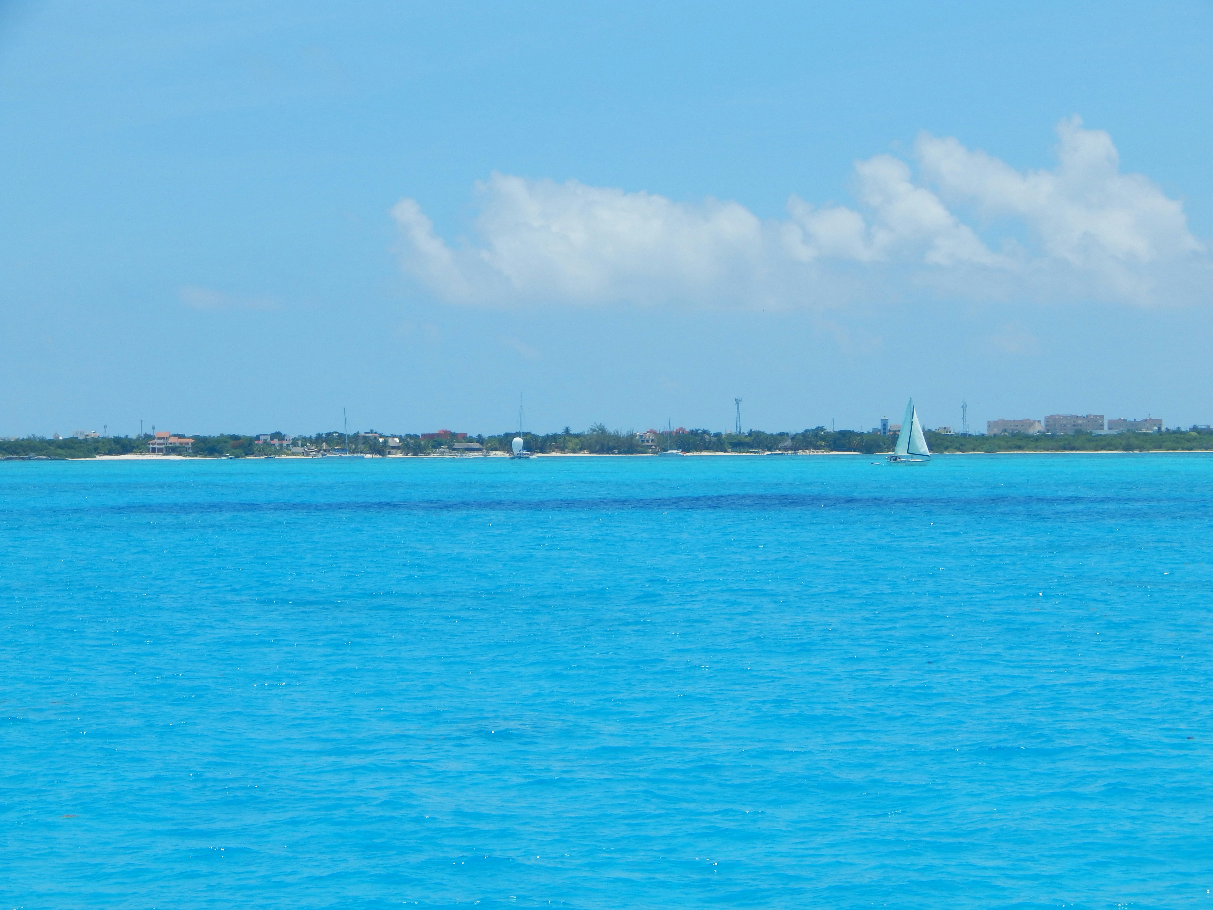A tranquil seascape featuring a sailboat gliding across vibrant turquoise waters, with a distant shoreline under a clear blue sky.