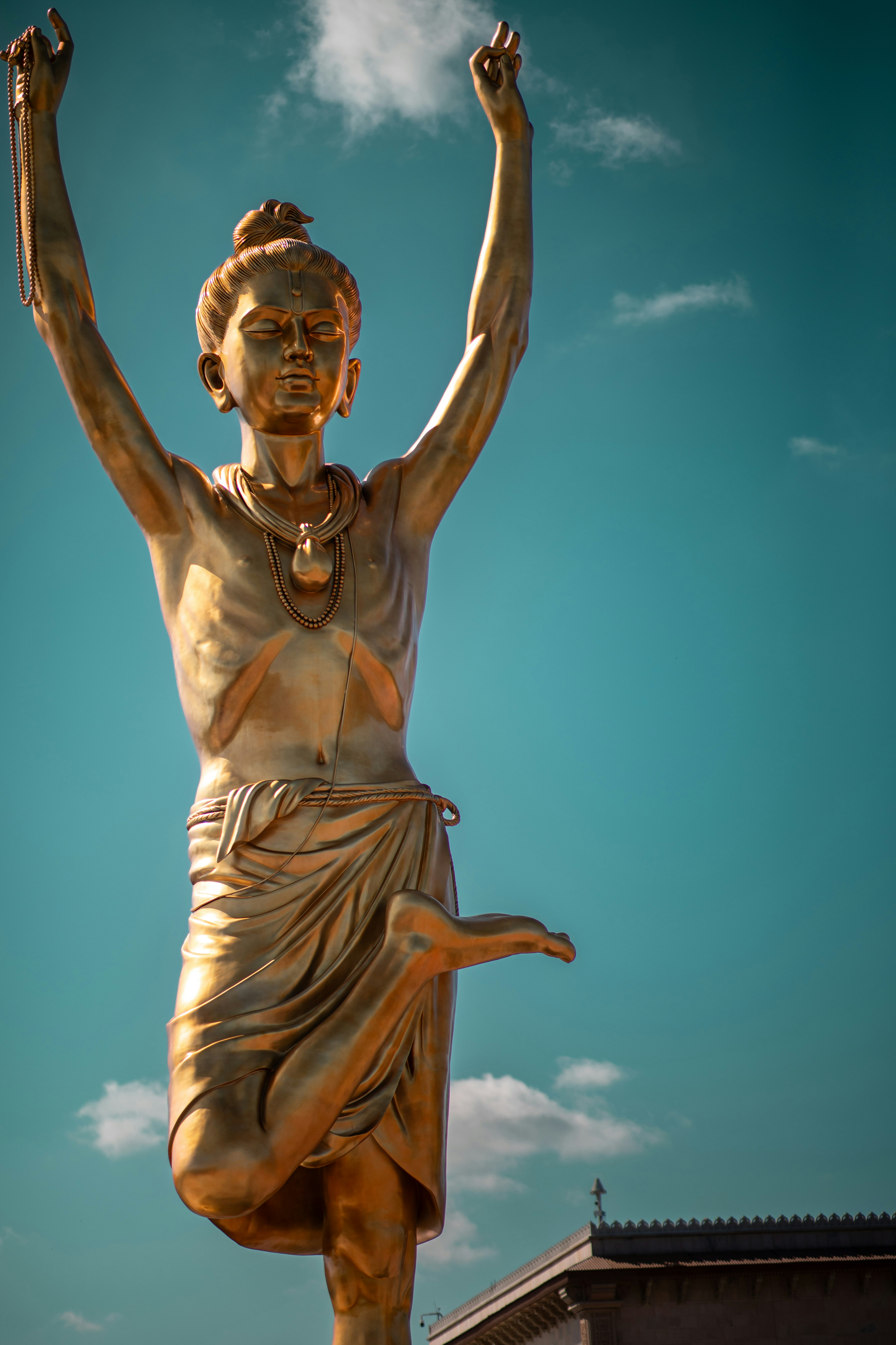 A majestic golden statue of a dancer, captured mid-leap, showcasing intricate details and vibrant colors against a clear blue sky.