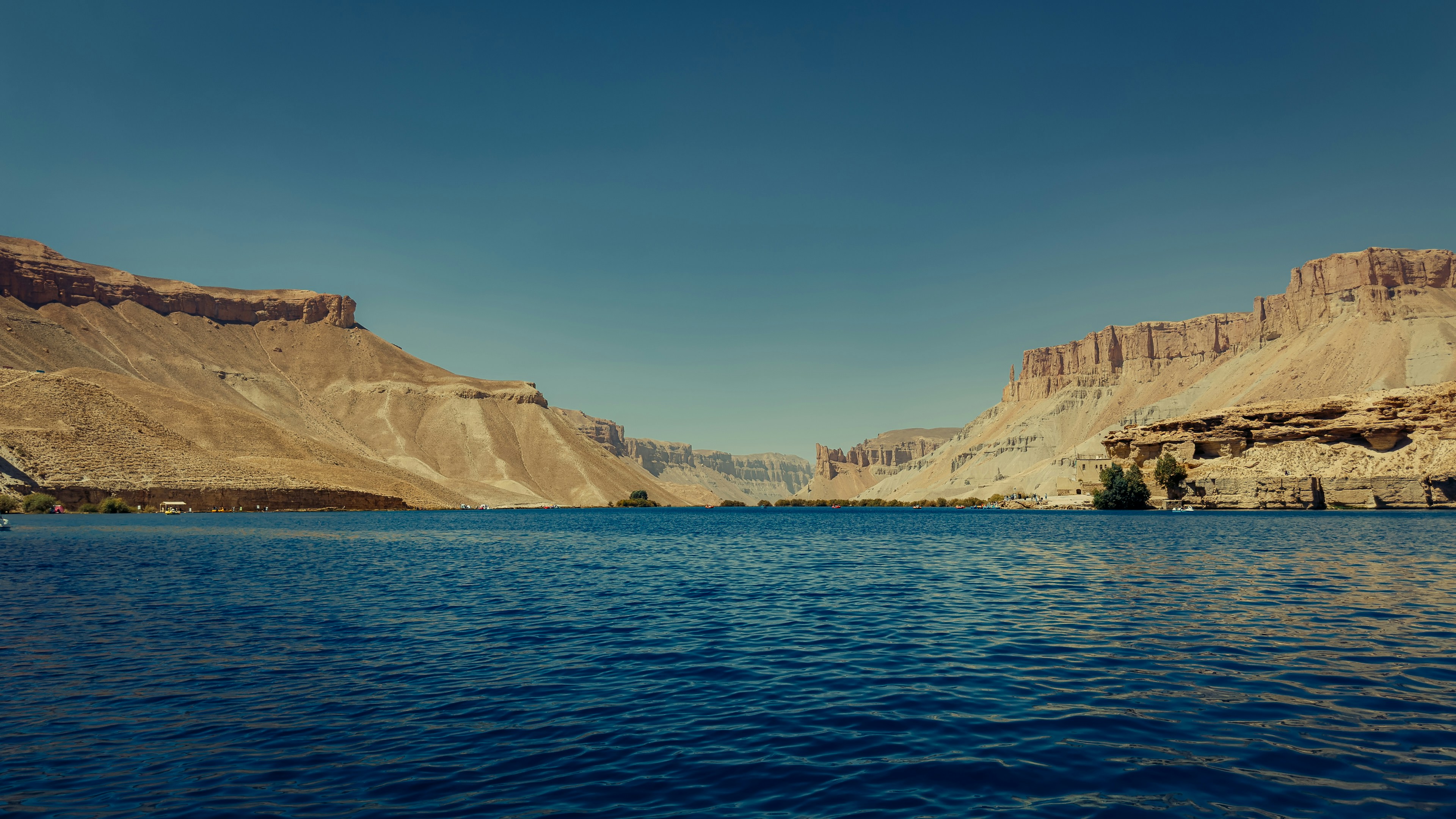 Expansive view of a tranquil lake bordered by towering cliffs under a clear blue sky.