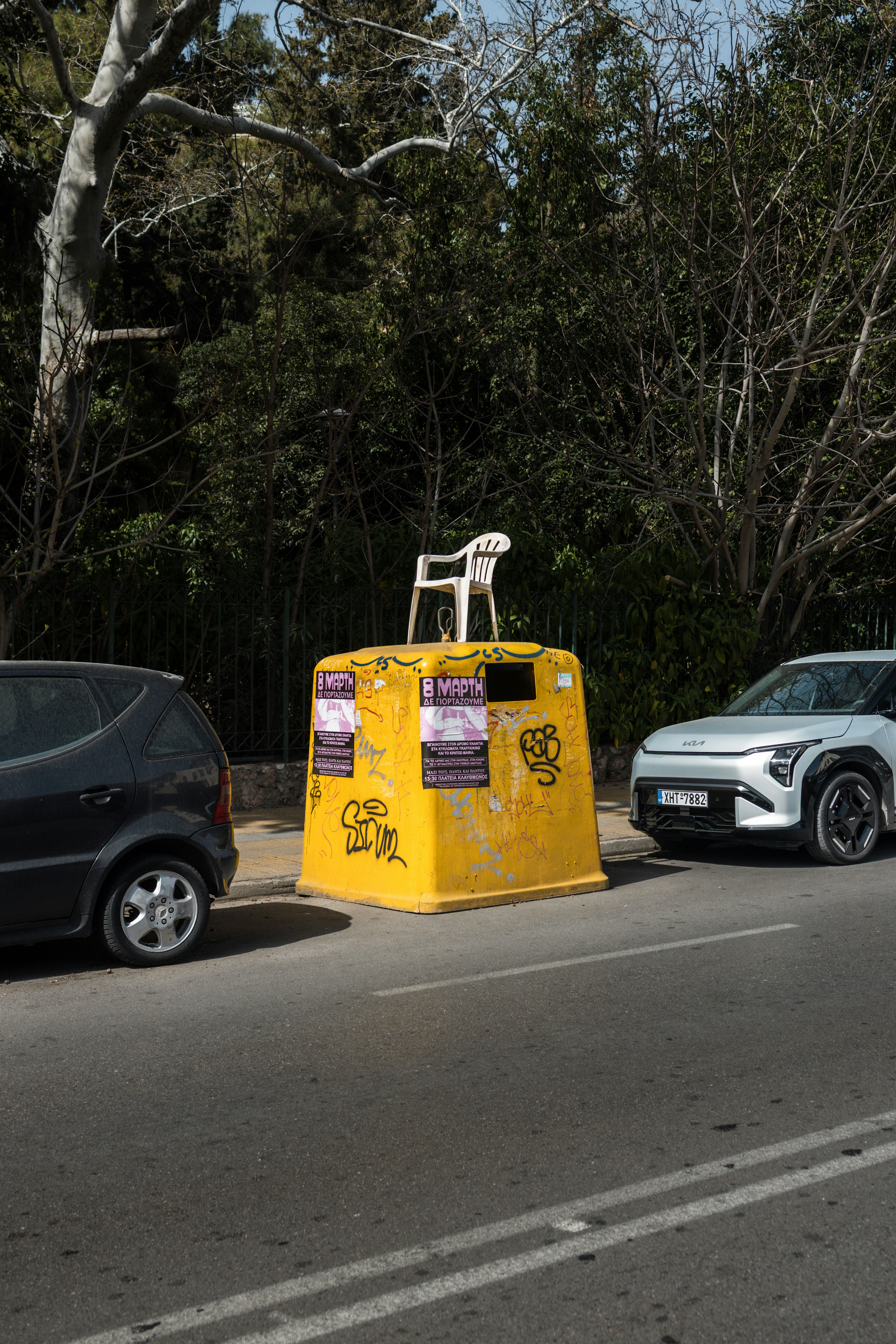 White chair sits atop a yellow dumpster on street.