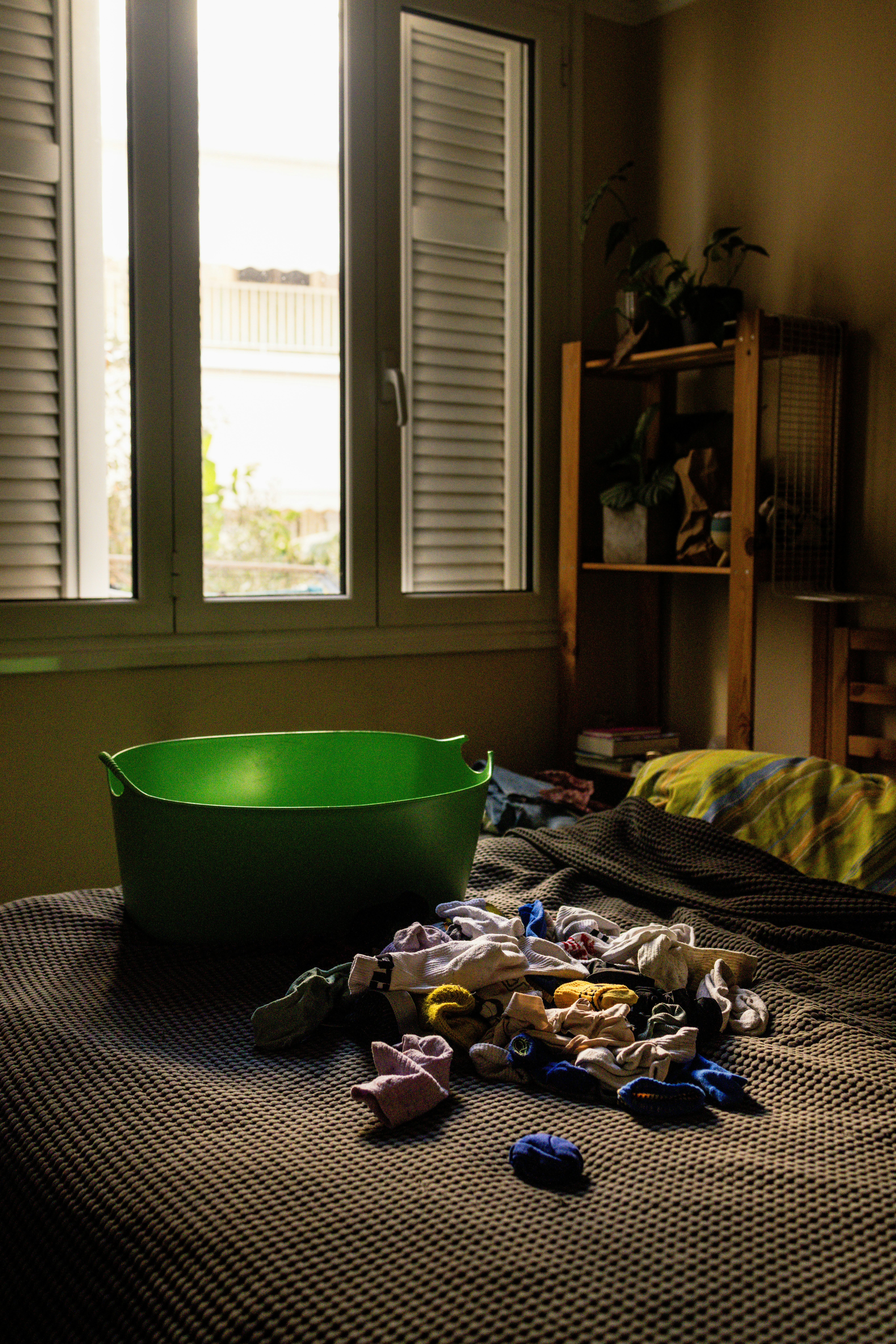 Green basin and pile of laundry on bed.