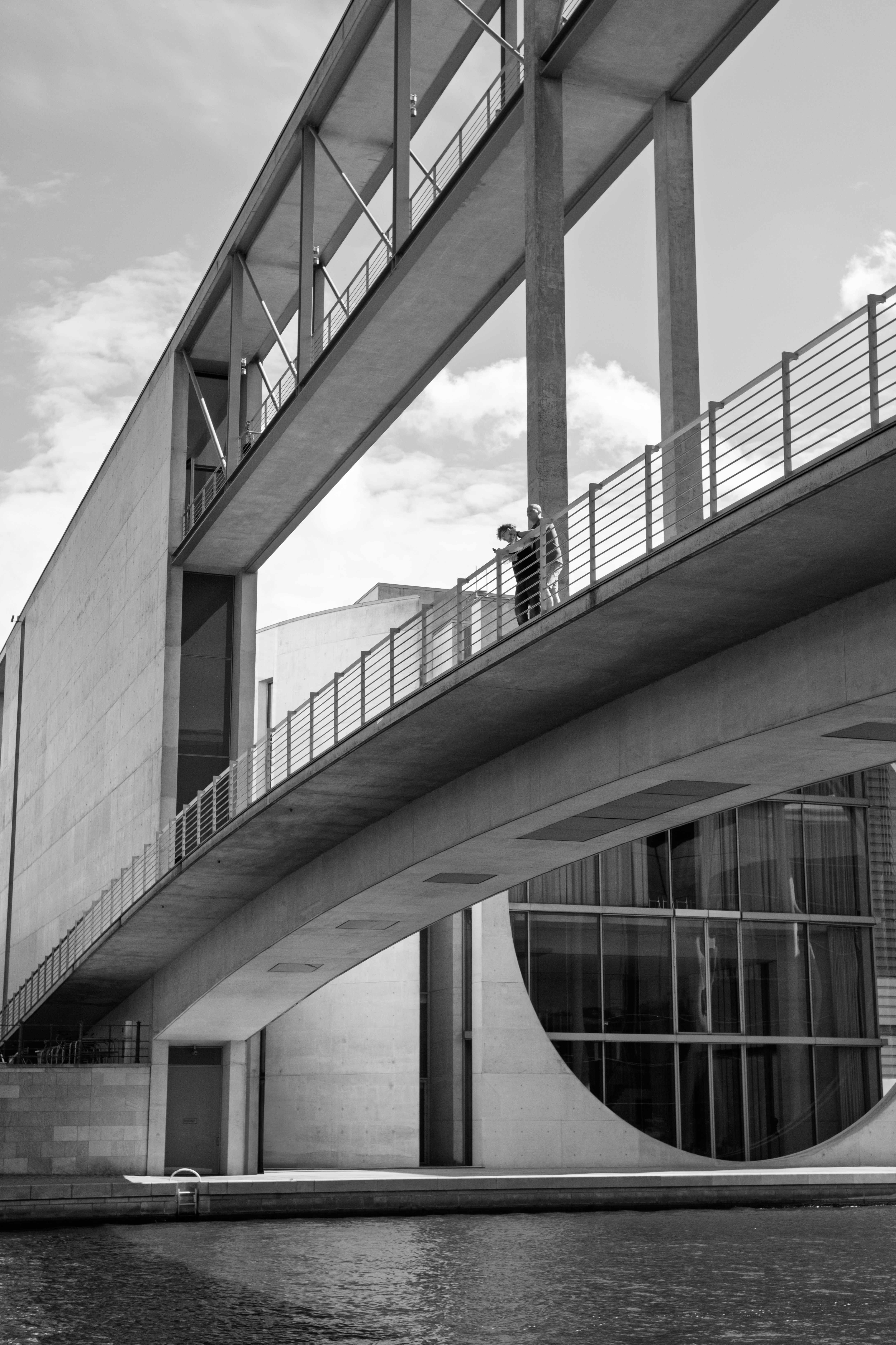 Two people on a modern concrete bridge over water.