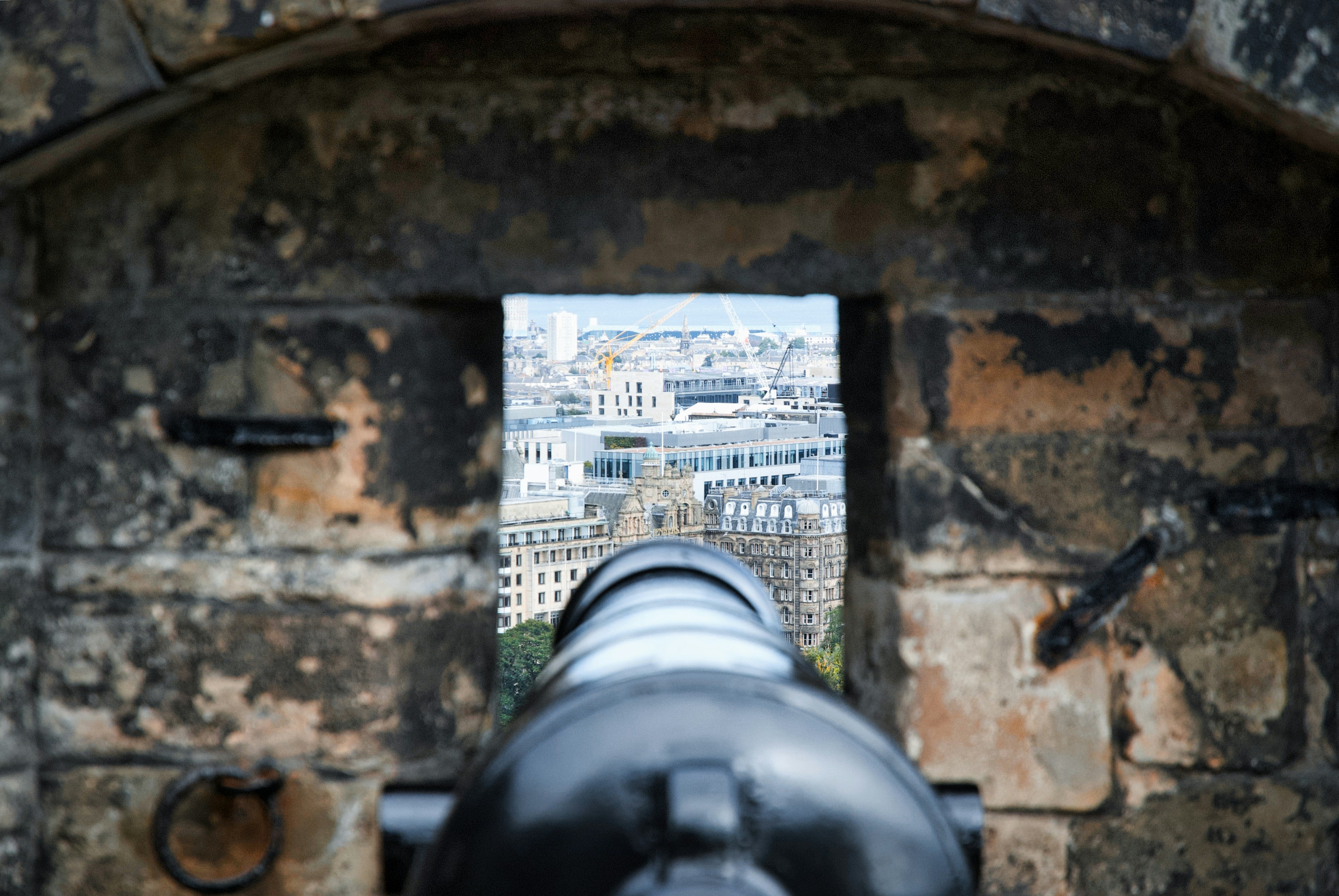 Cannon barrel pointing towards a city through a stone opening