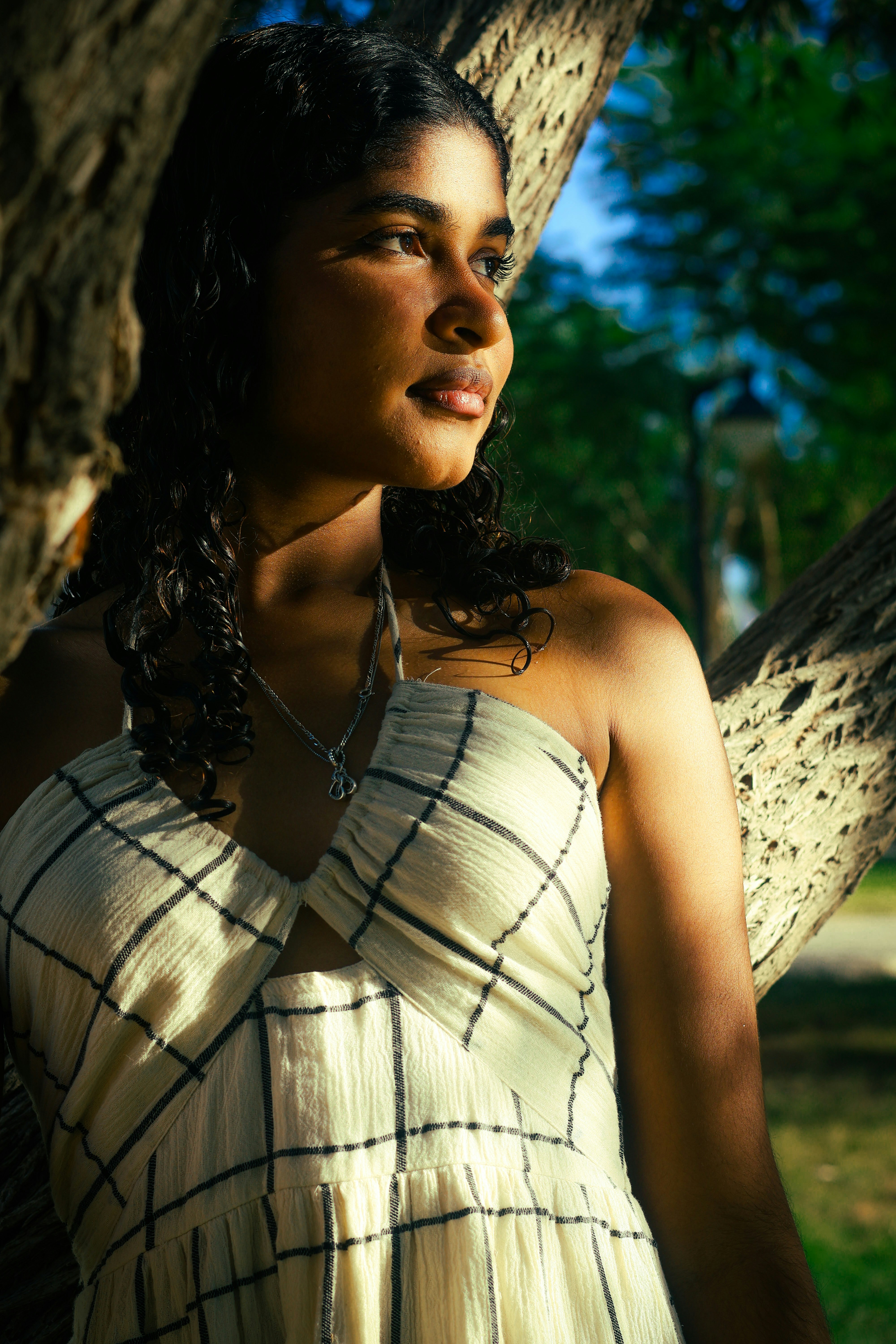 Young woman in a checkered dress by a tree.
