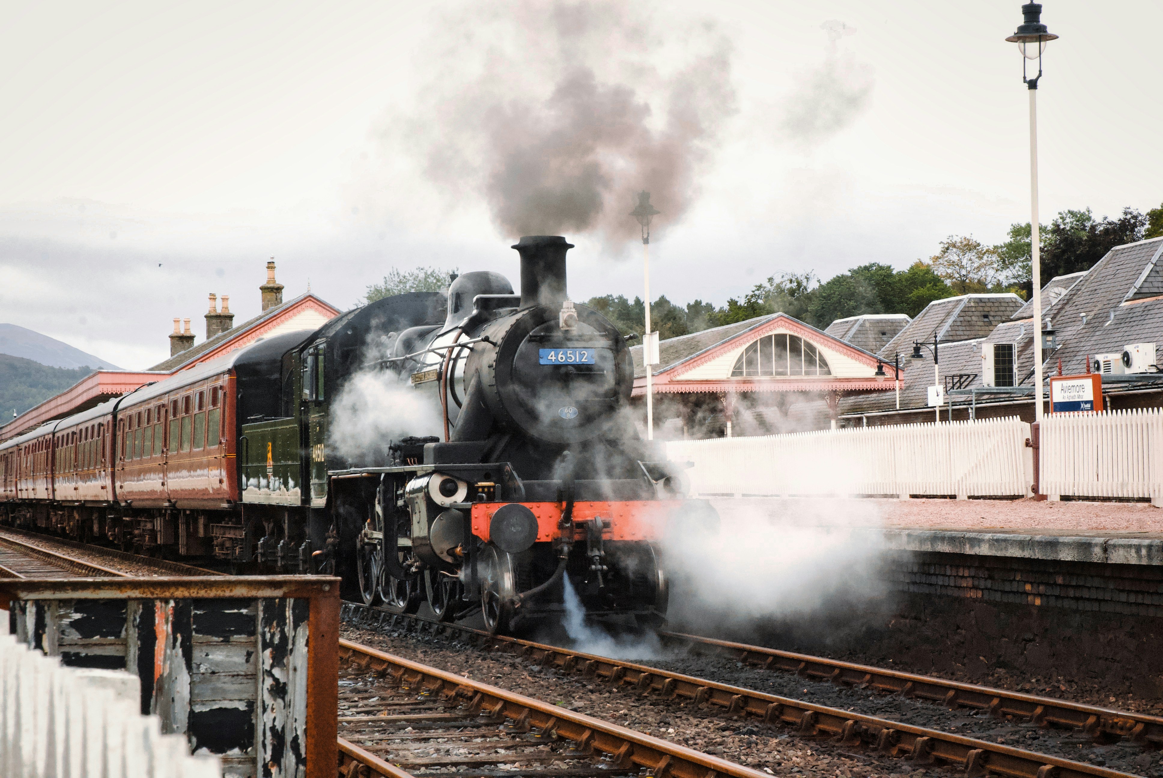 Vintage steam locomotive billowing smoke as it prepares to depart from a charming train station. The scene captures the essence of nostalgic rail travel.