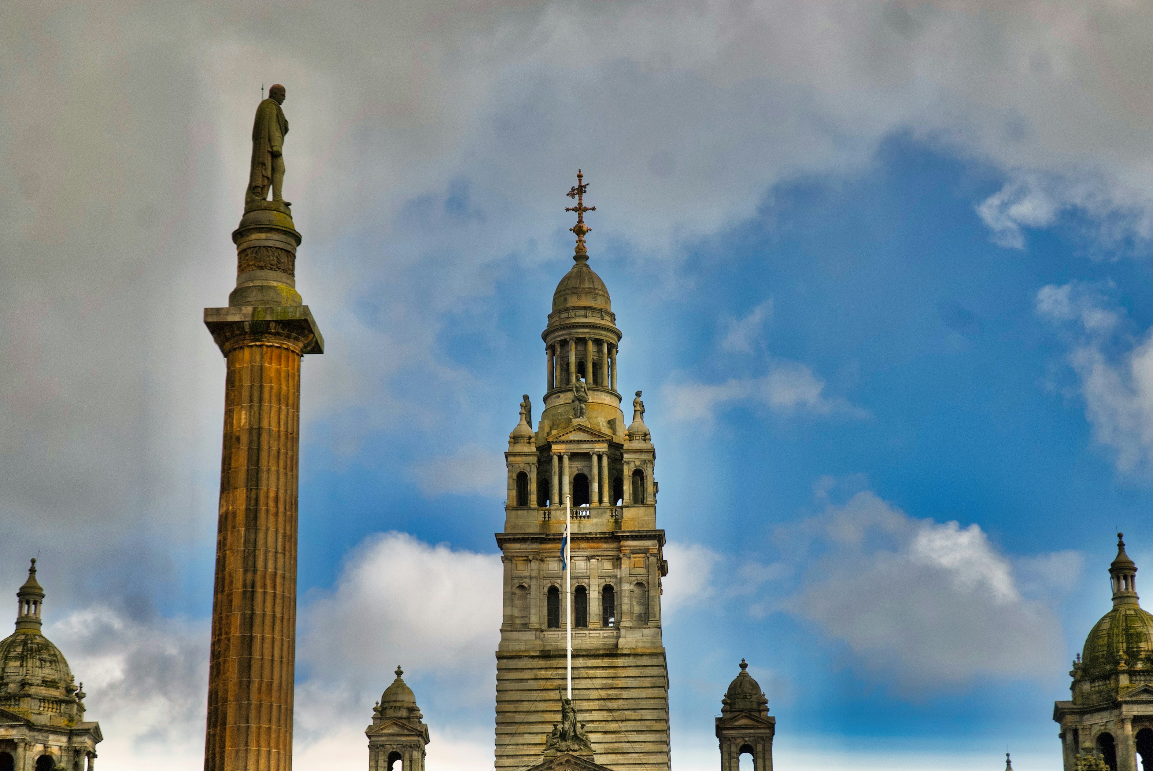 Tall column and ornate tower against cloudy sky