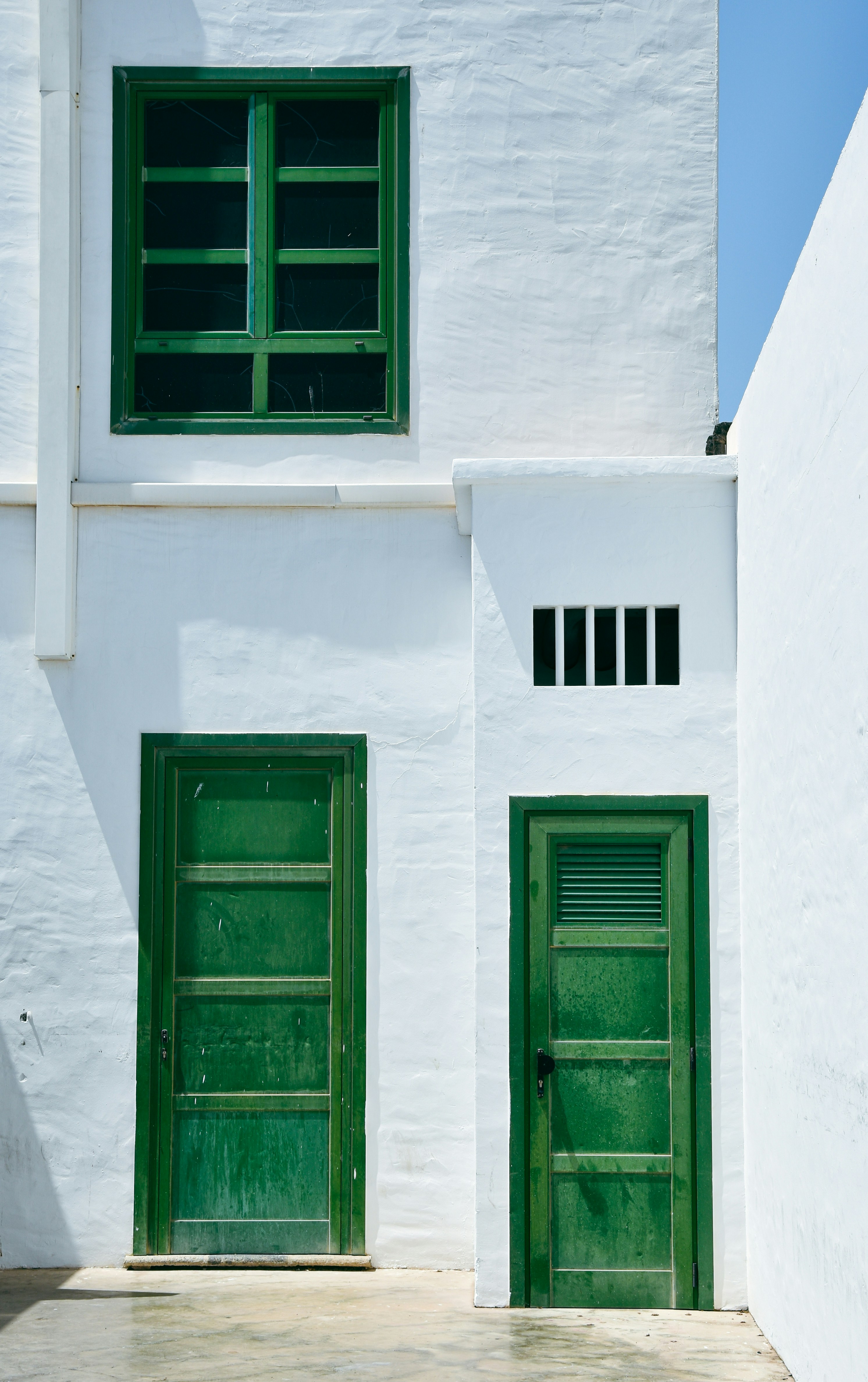 Two green doors and a window on a white wall