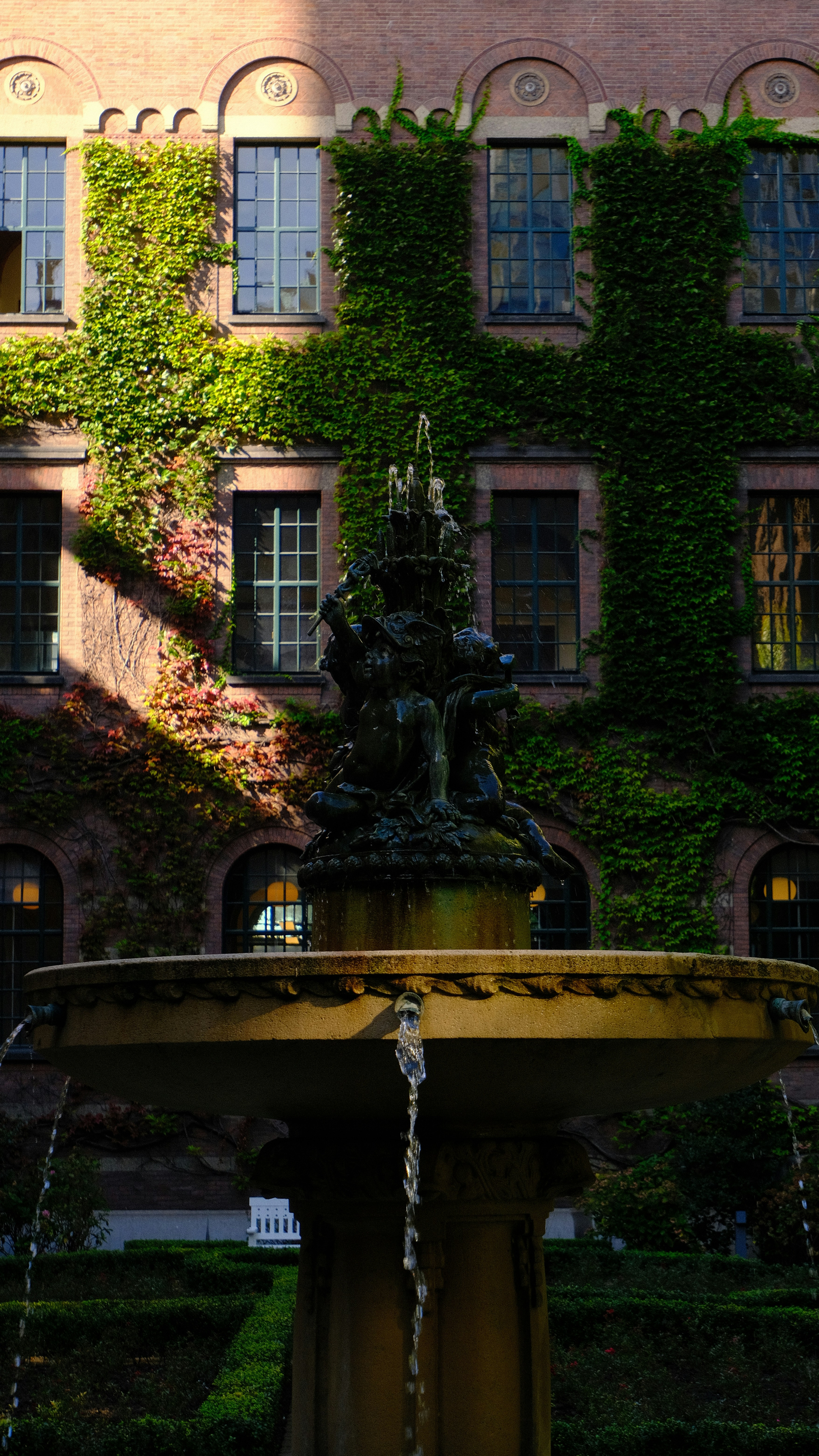 Fountain in courtyard with ivy-covered building.