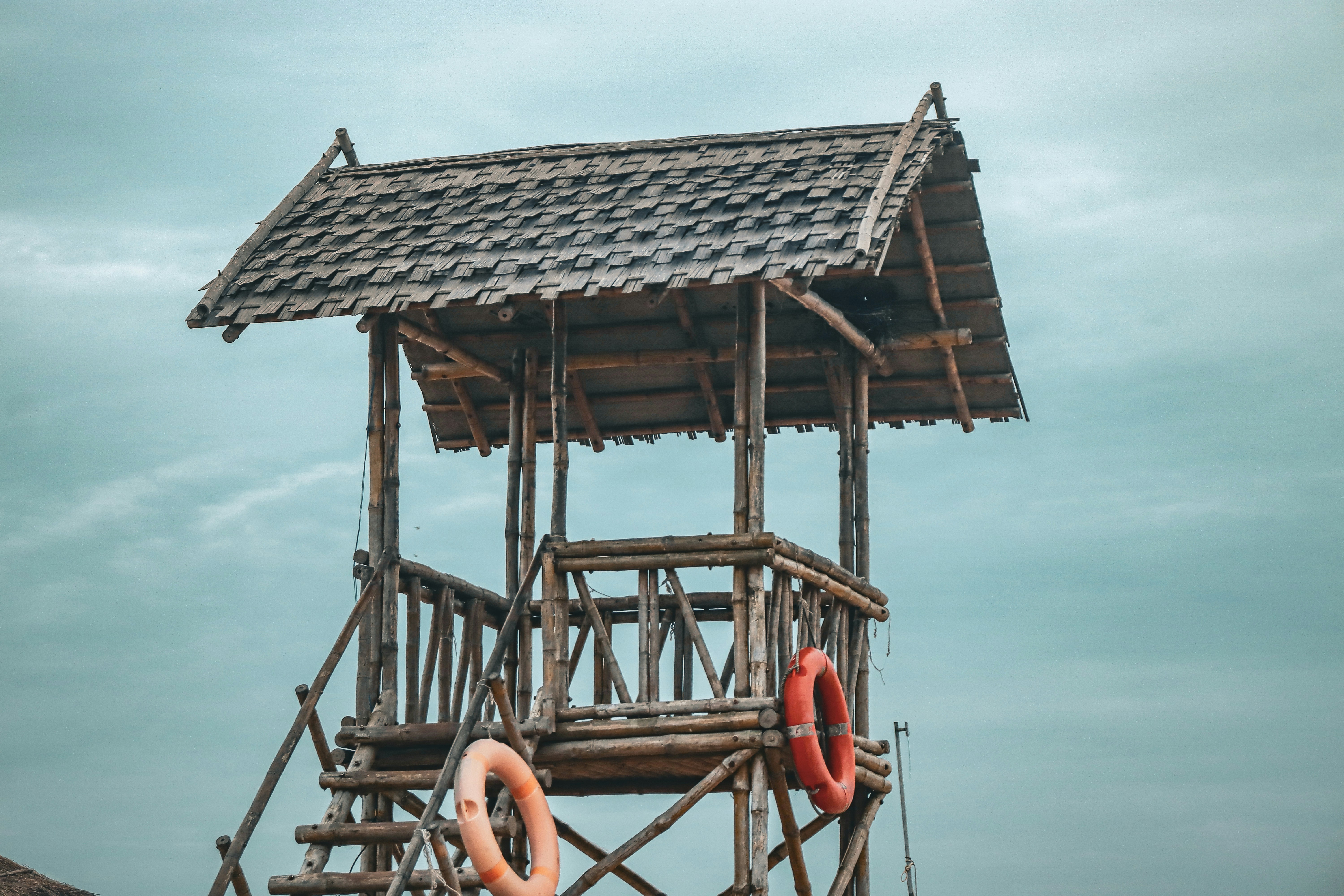 Wooden lifeguard tower with a thatched roof, featuring bright orange life rings against a moody sky.