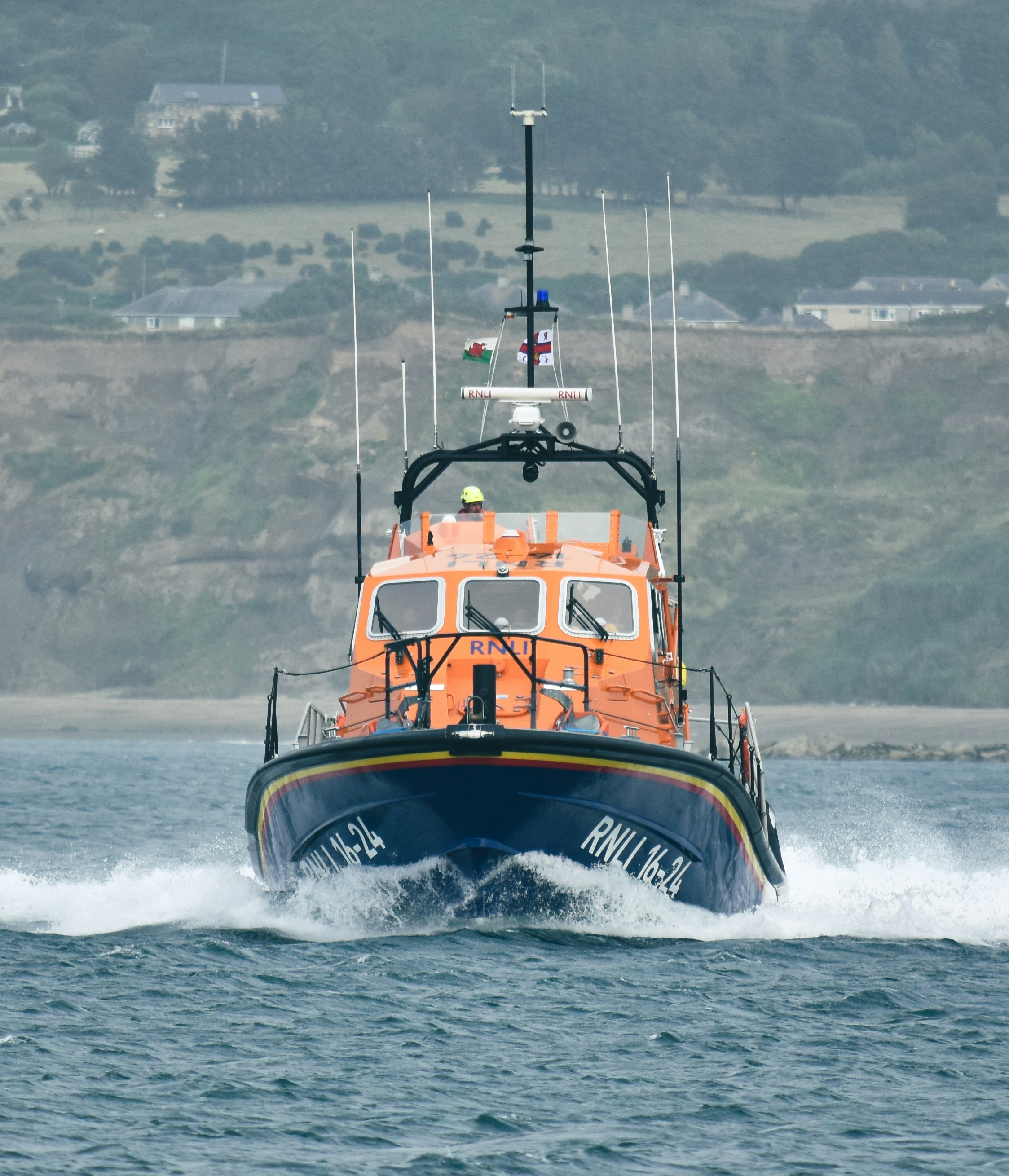 The Royal National Lifeboat Institution's rescue boat off the Morfa Nefyn coast in North Wales. The RNLI is a charity that saves lives at sea in the UK and Republic of Ireland by providing a lifeboat search and rescue service, deploying lifeguards on beaches, and educating the public on water safety. | Orange and blue lifeboat speeding through choppy water