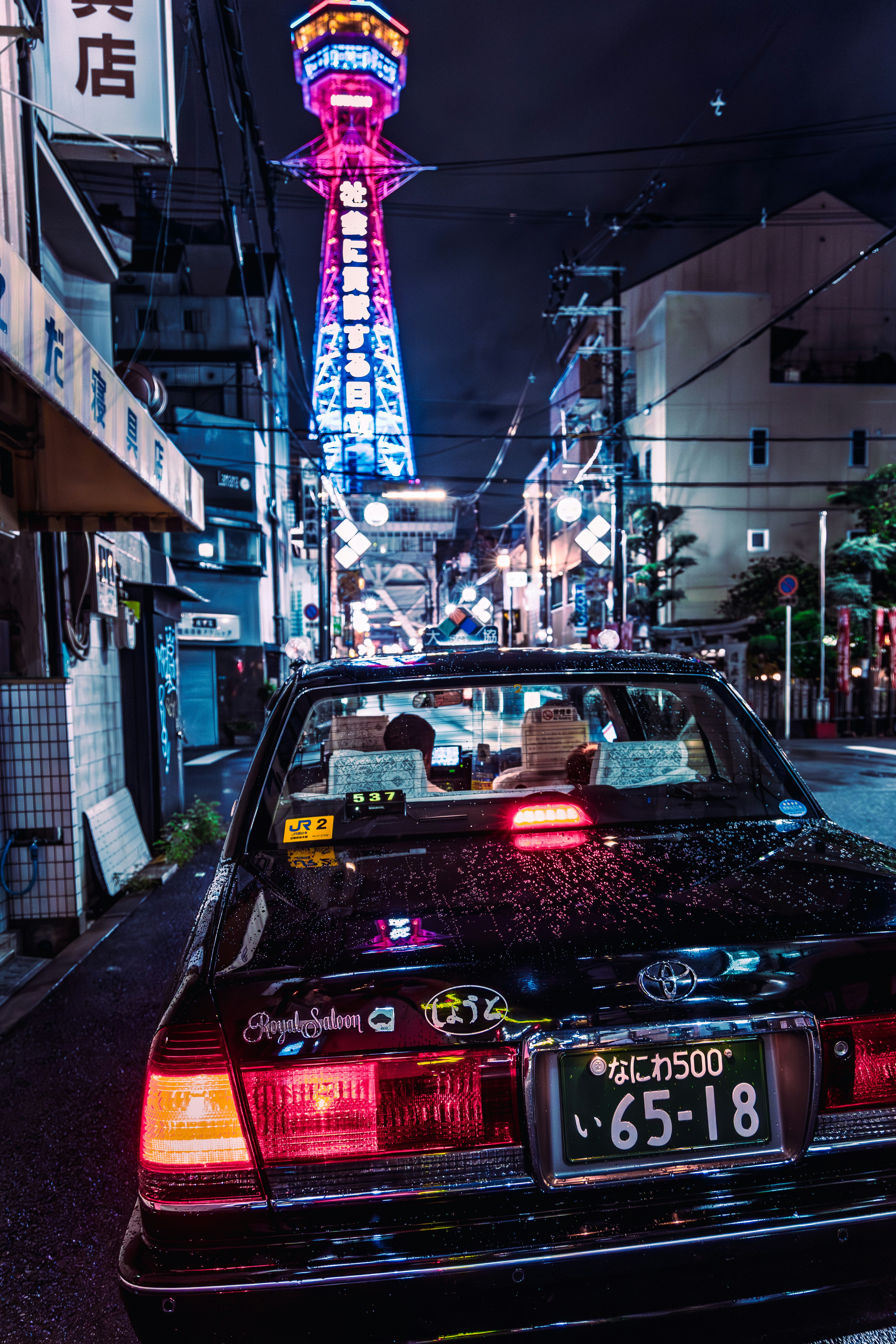 Neon Tower Over a Rain-Kissed Osaka Street: Taxi Lights in Night Drift