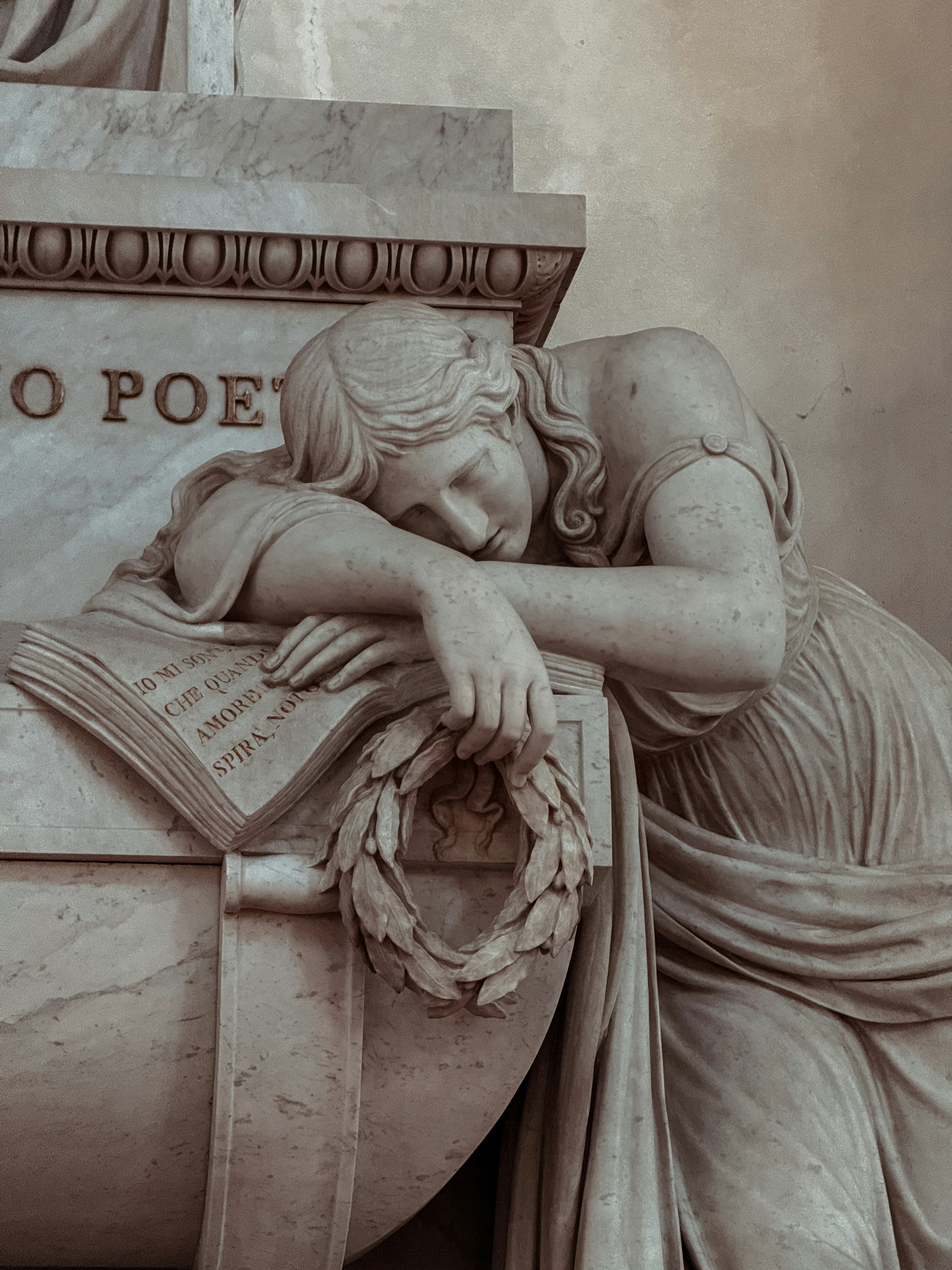 A marble sculpture depicting a contemplative figure resting on an open book, adorned with a laurel wreath, symbolizing poetic inspiration.