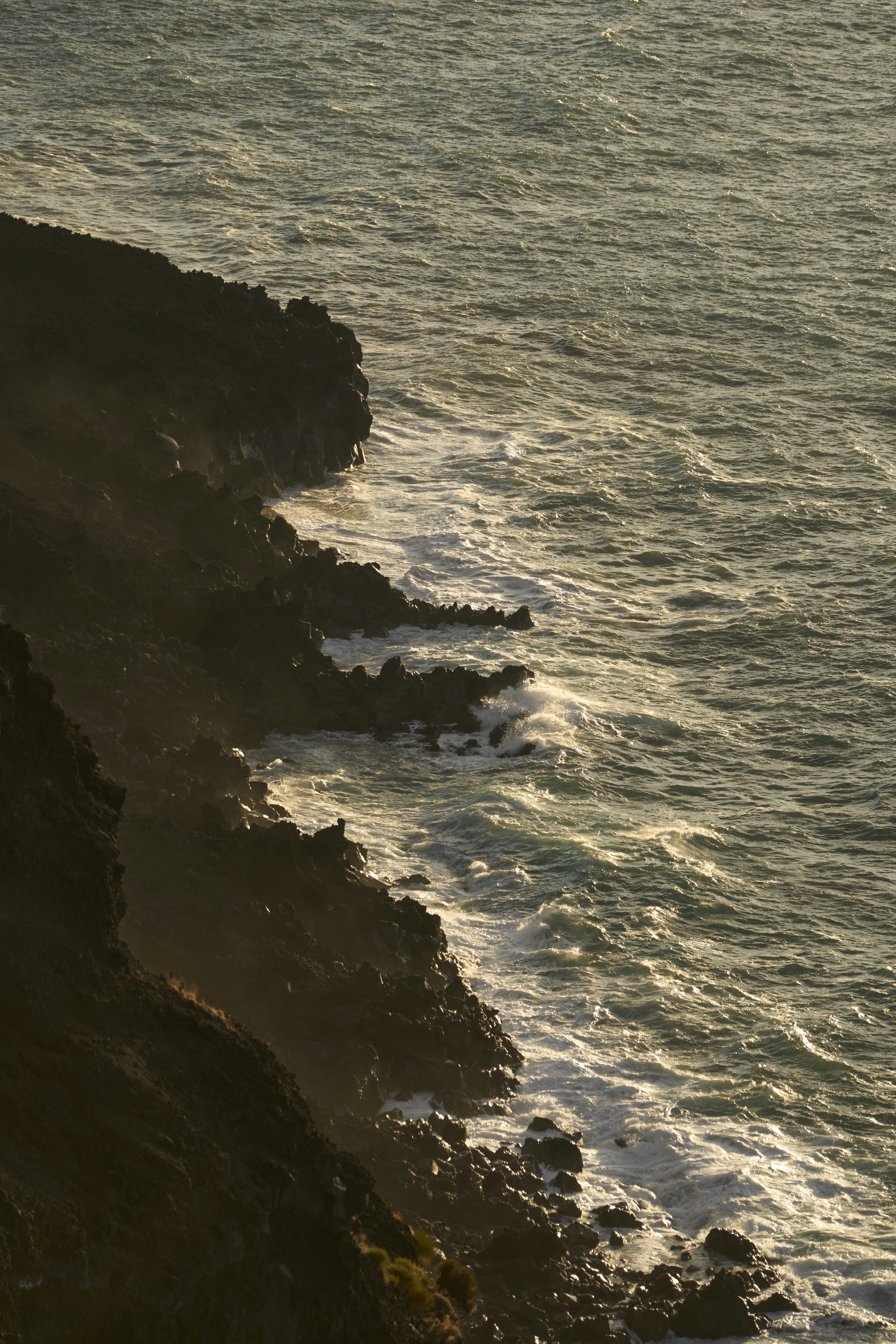 Waves crash against a rocky coastline at sunset.