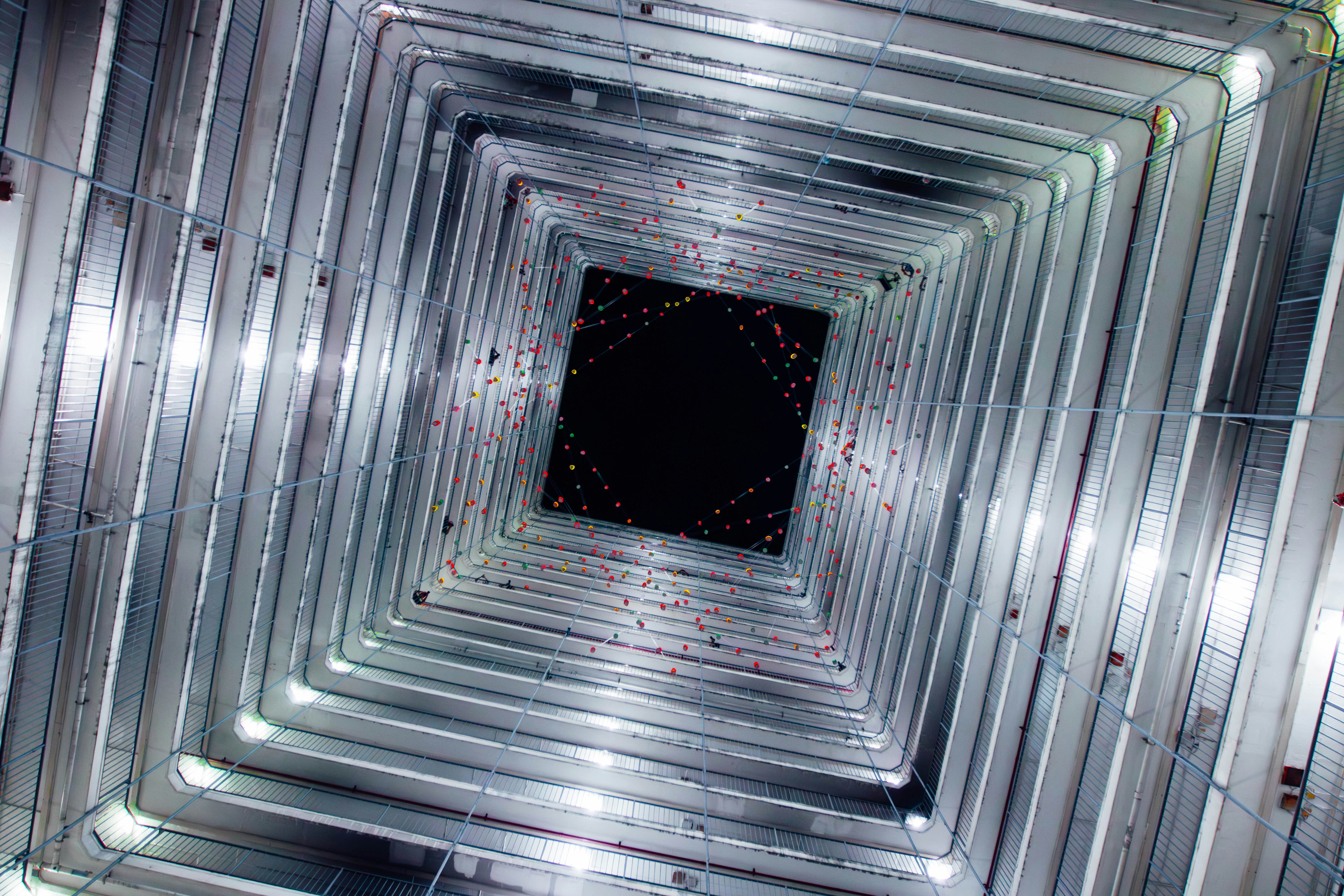 Looking up through a square building shaft with lights.
