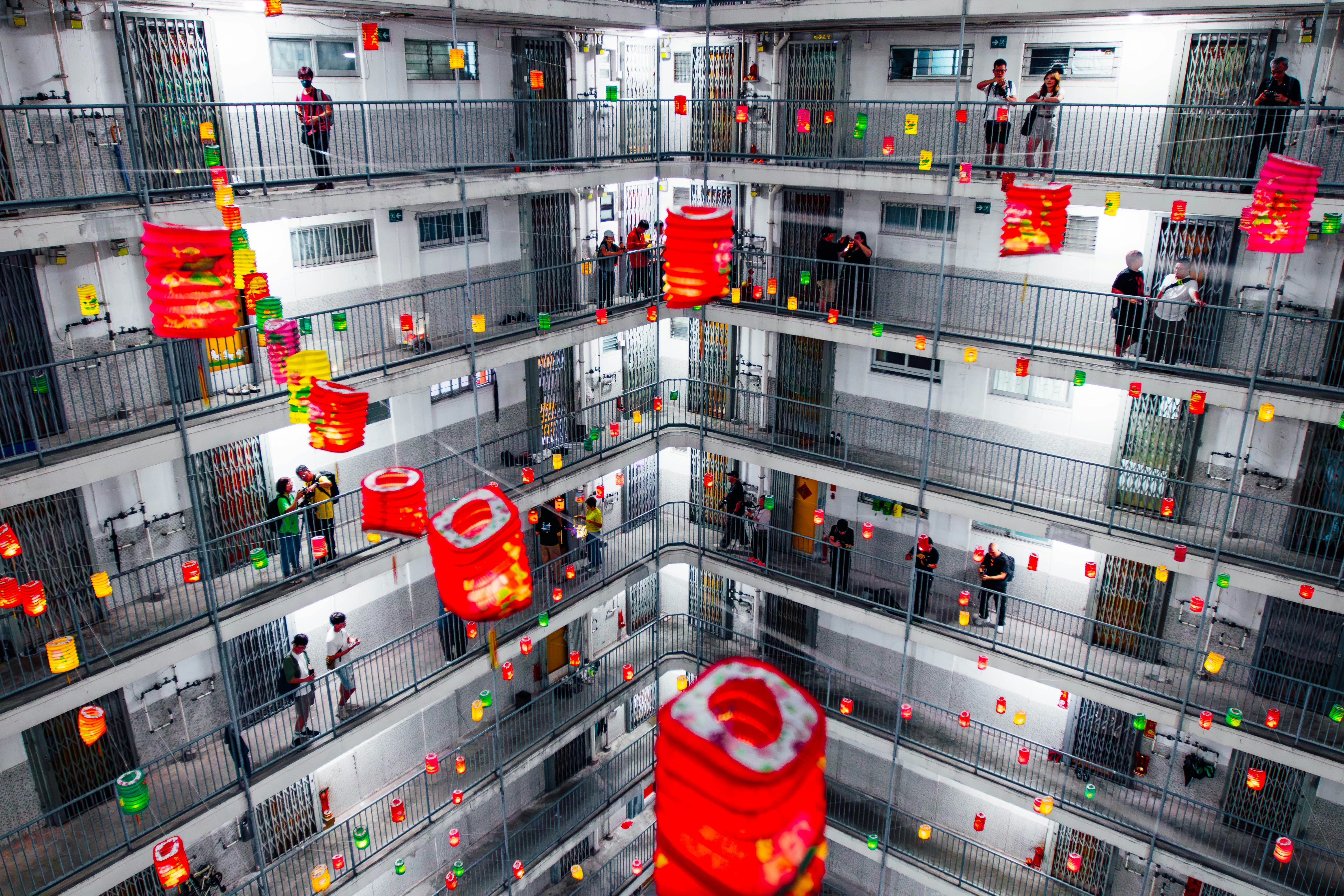 Vibrant paper lanterns hang in a multi-story residential building, illuminating the communal space where residents engage with one another.