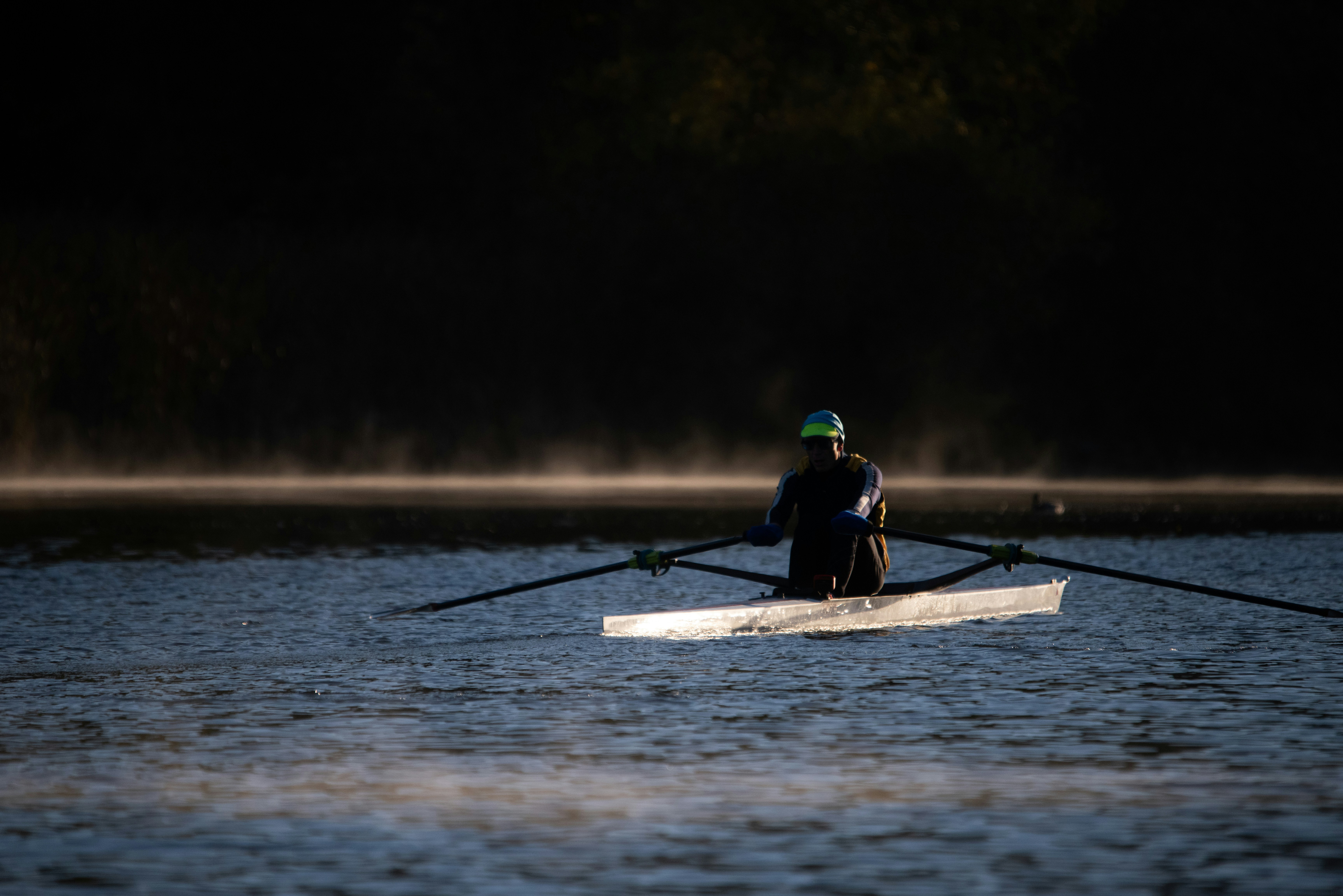 A lone rower glides across a misty lake at dawn.