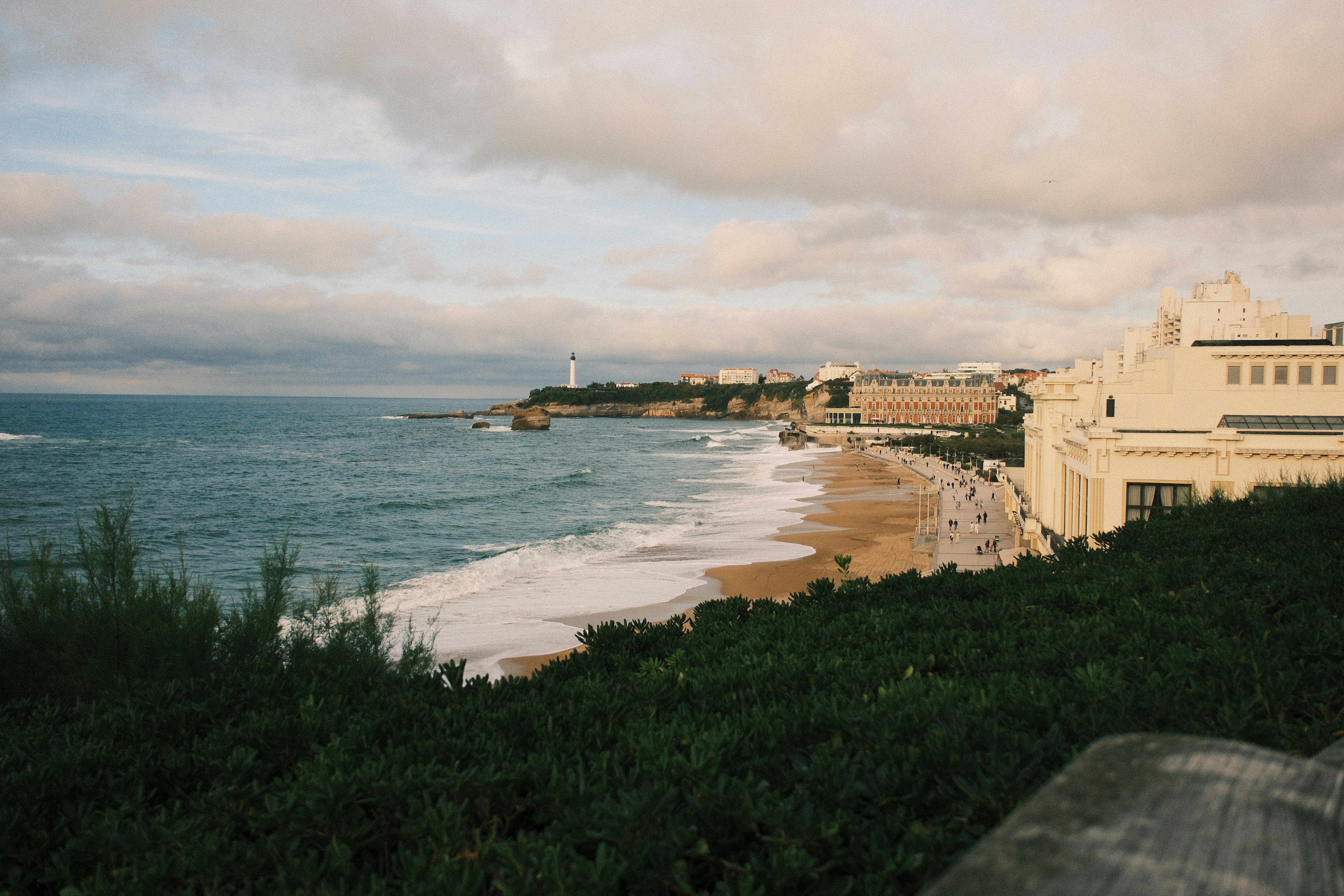 Waves crash on a sandy beach with buildings beyond.