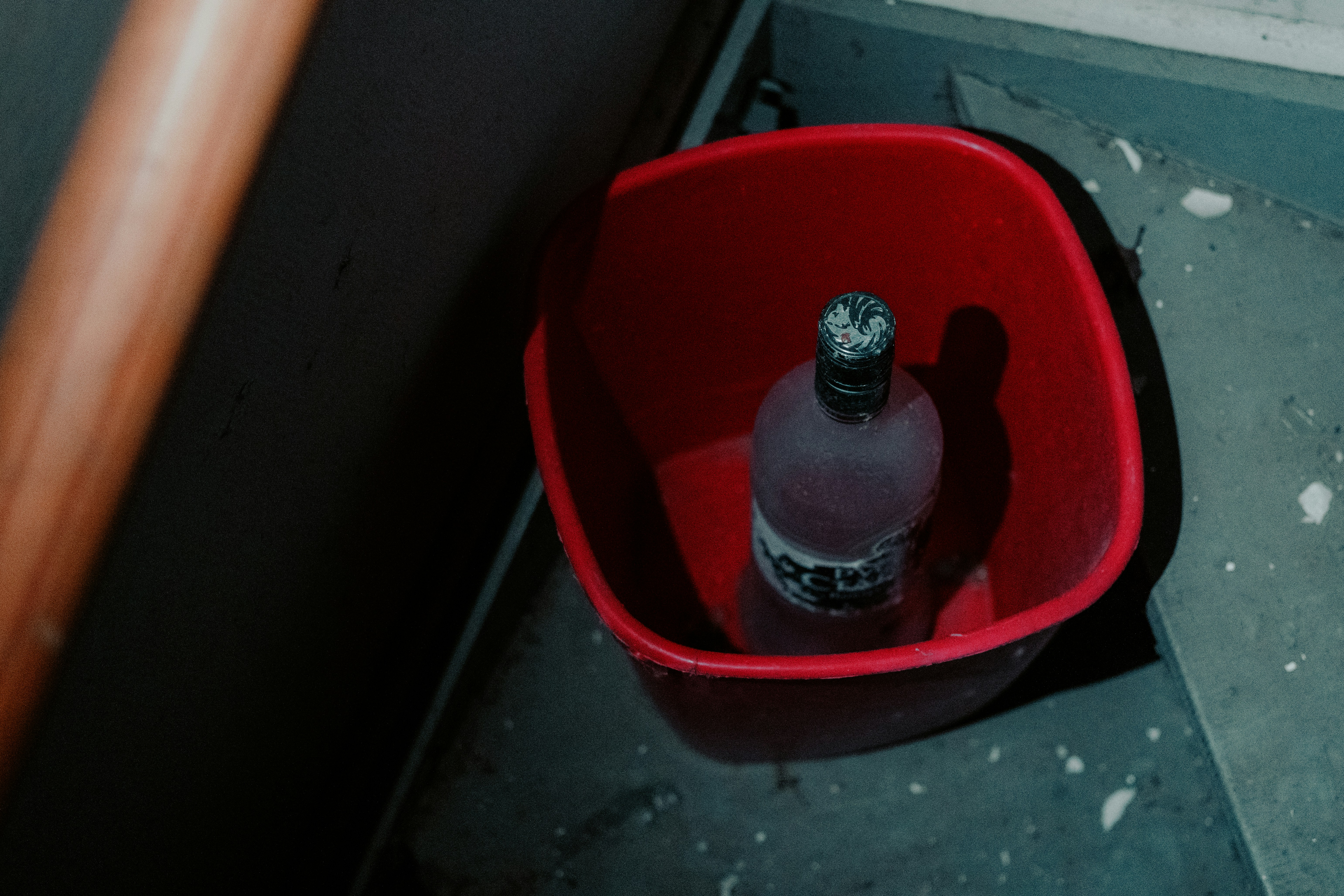 Bottle inside a red bucket on the floor.