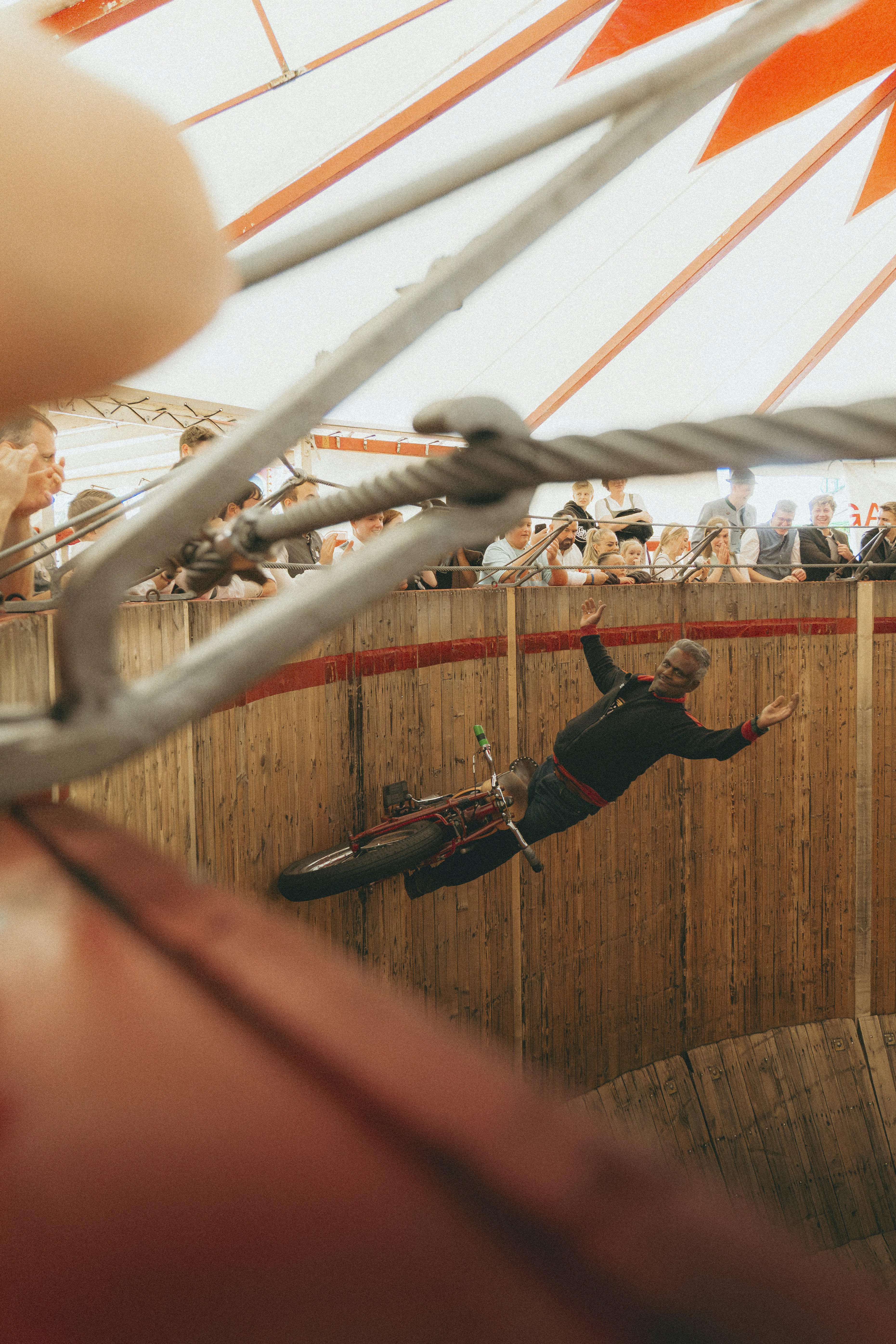 Motorcyclist rides up wooden wall of death arena.