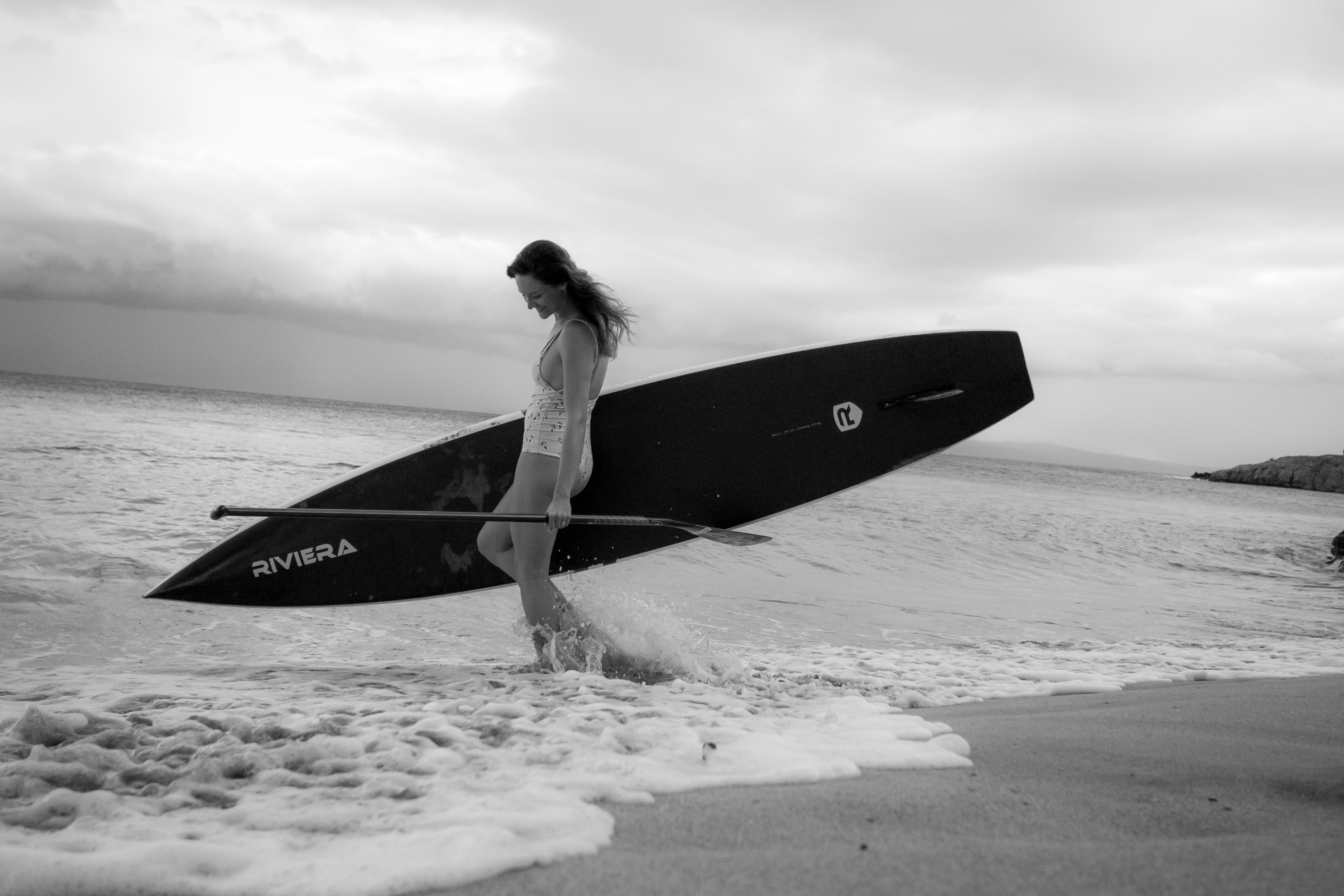 Woman walking on beach carrying surfboard and paddle