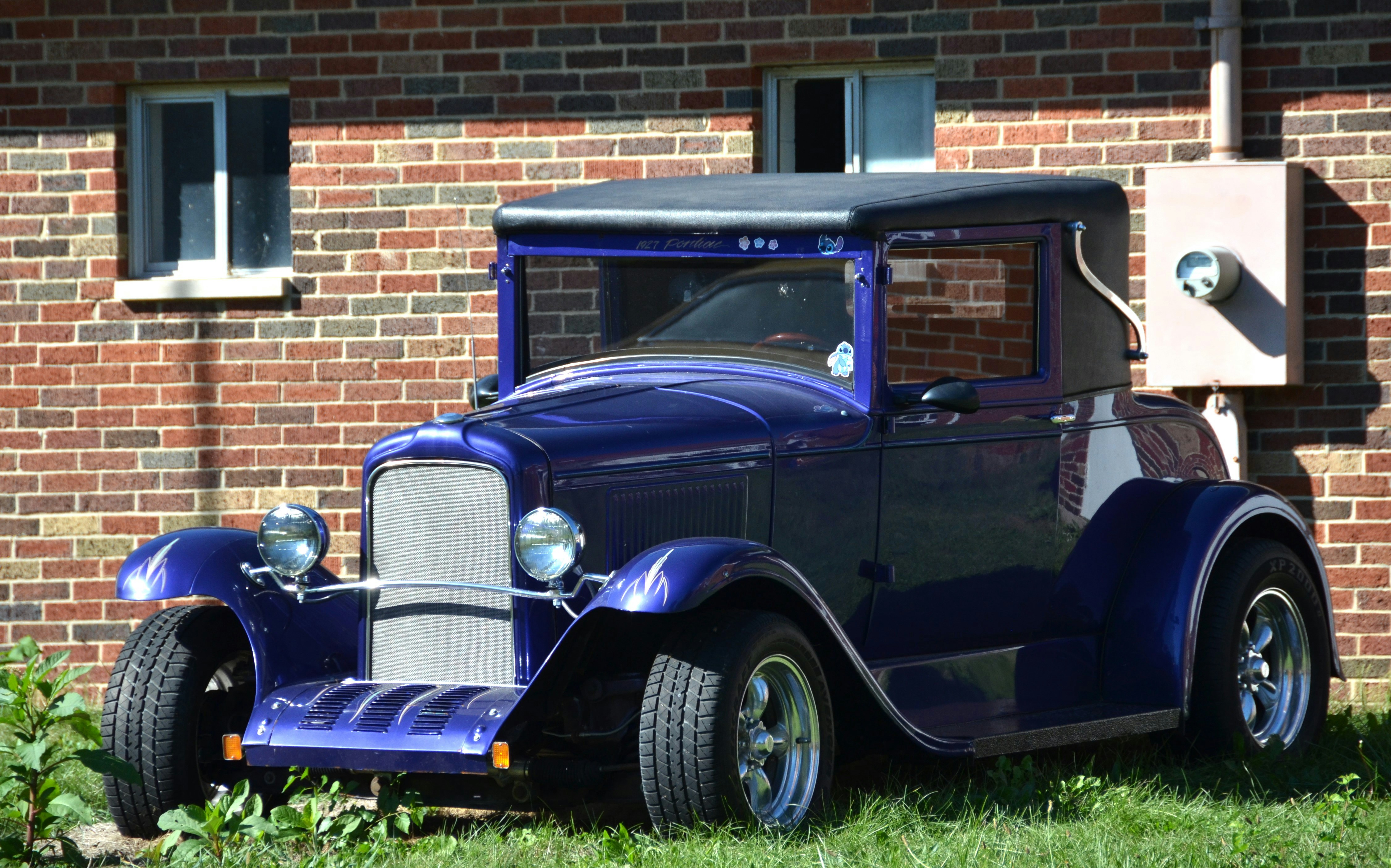 A classic purple car parked beside a brick wall, showcasing its vintage design and gleaming chrome details.