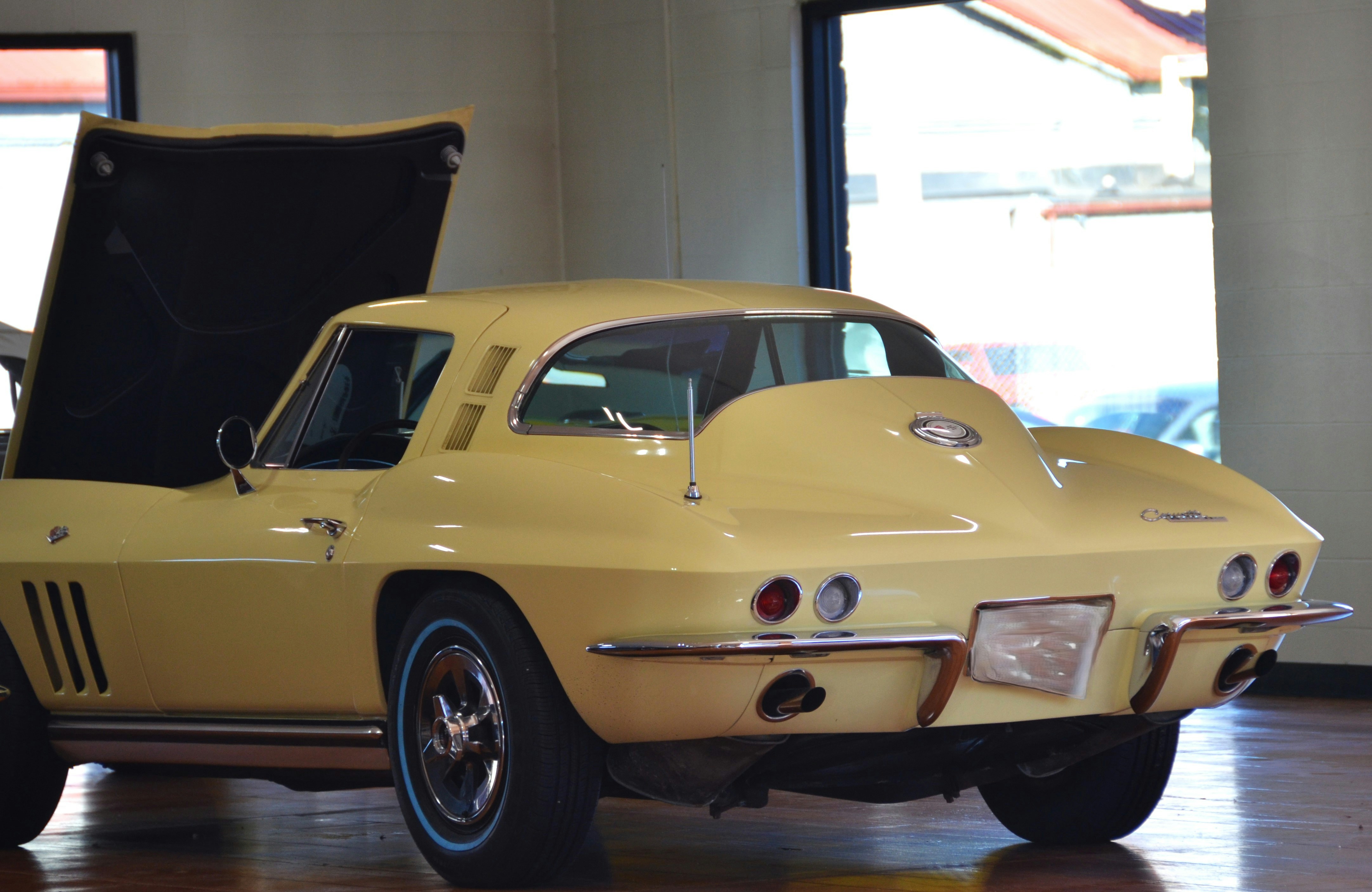 Vintage yellow Corvette with its hood raised, showcasing its classic design and detailing. The gleaming chrome accents highlight its iconic status.