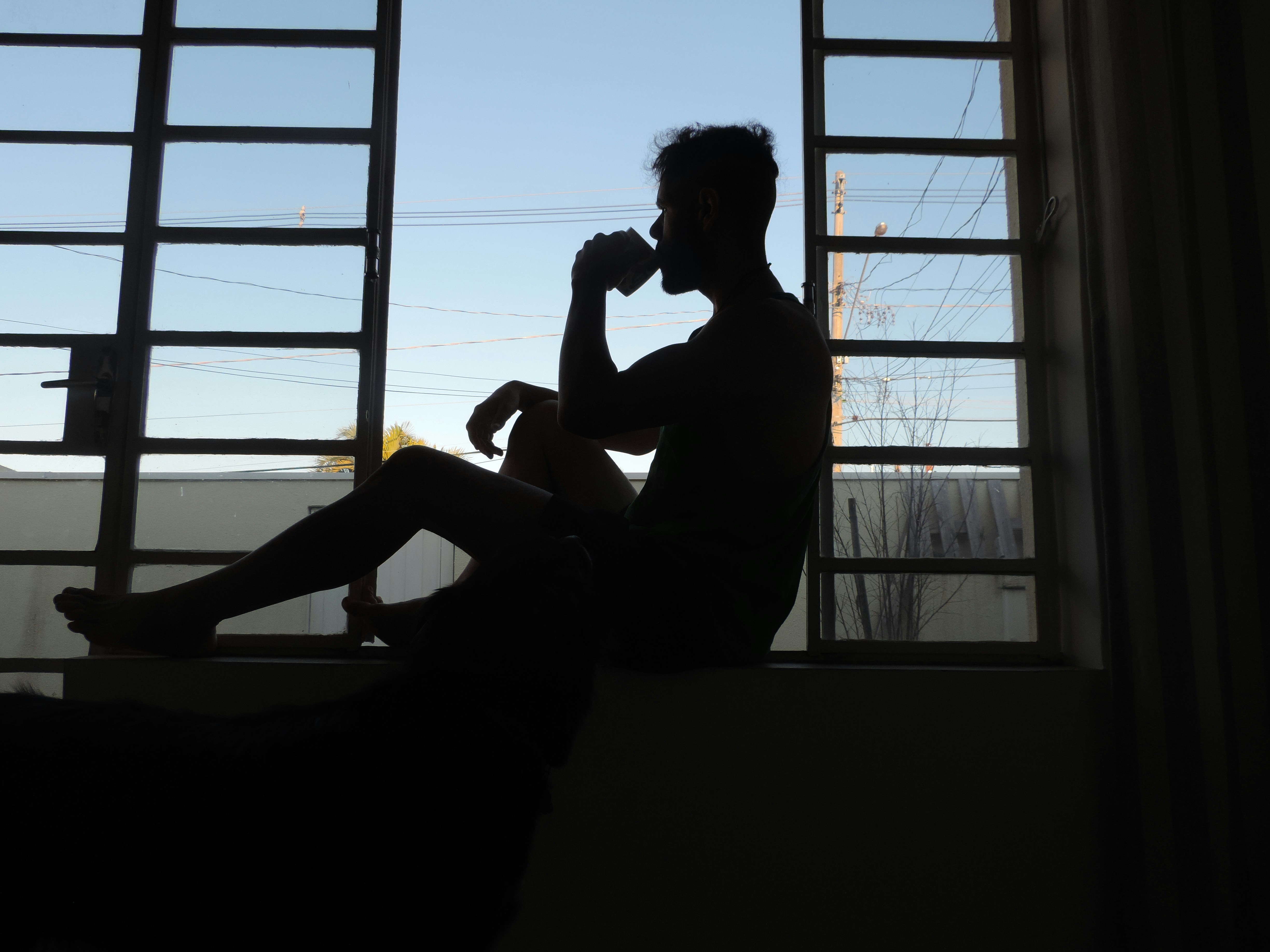 Silhouette of a person drinking coffee by the window.