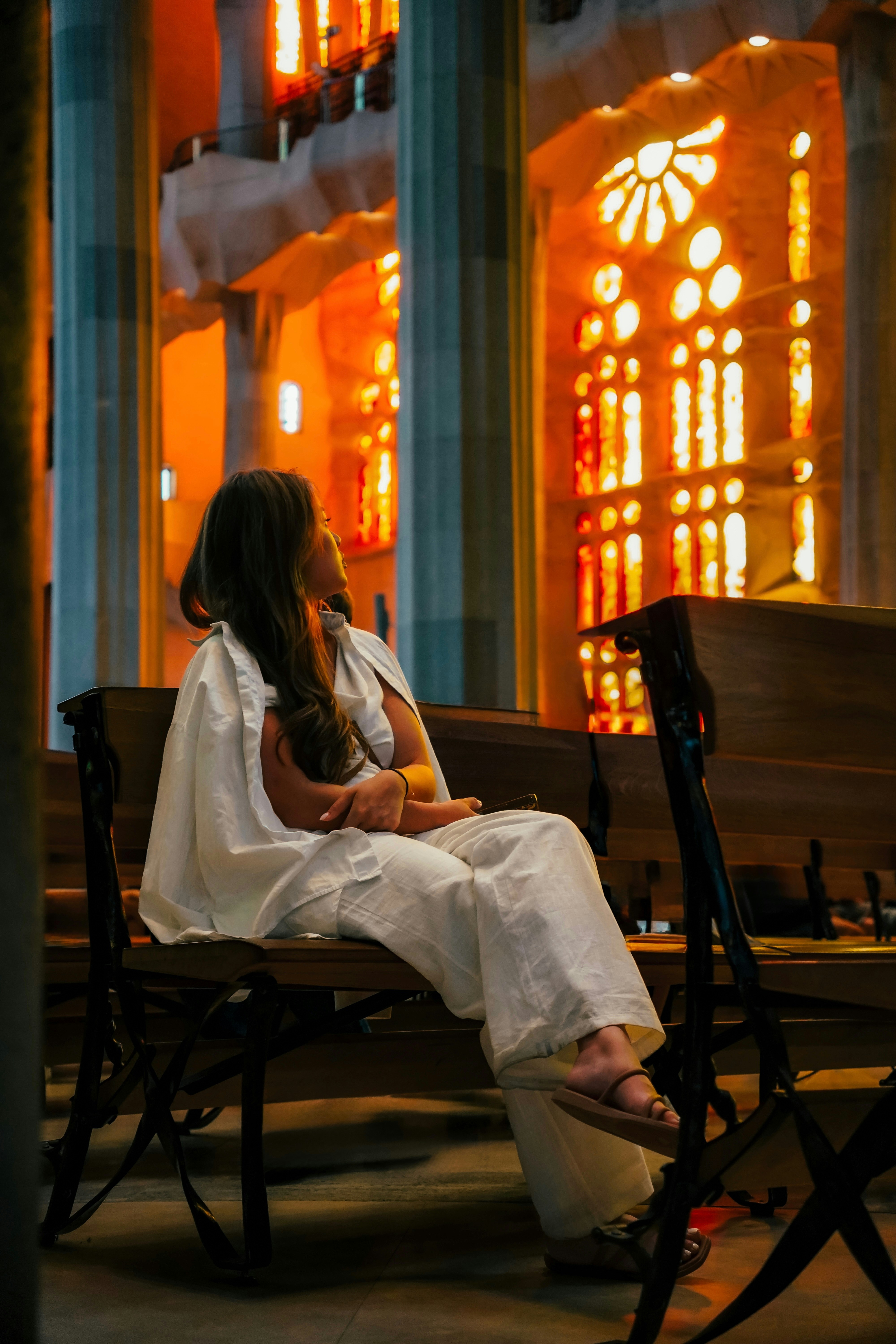 Woman sitting on bench in church with stained glass.