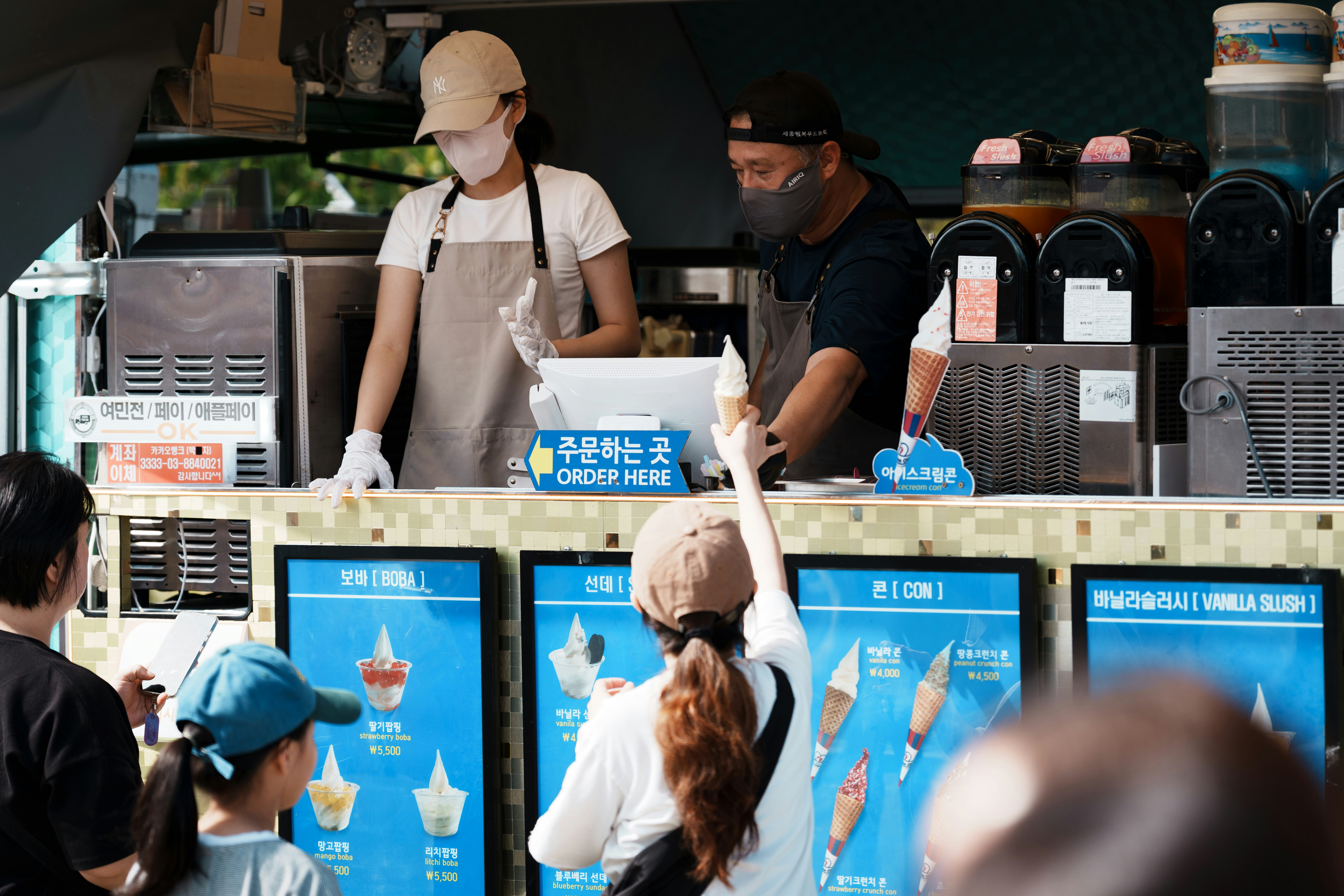 Busy ice cream stand with staff serving customers, showcasing a variety of colorful ice cream options on display.