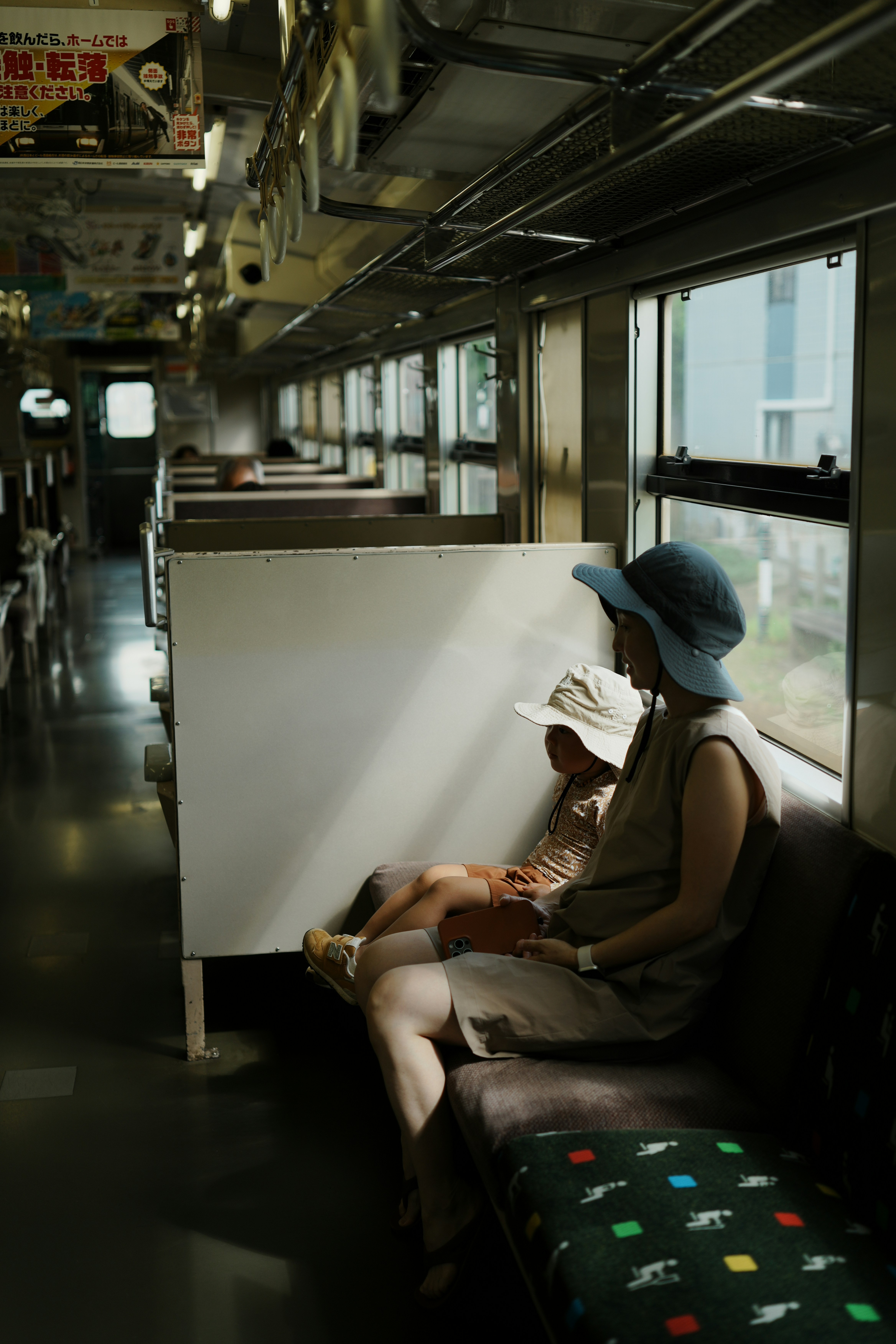 A woman and a child sit quietly in a sunlit train carriage, embodying a serene moment of companionship. The interior features vintage decor and soft shadows.
